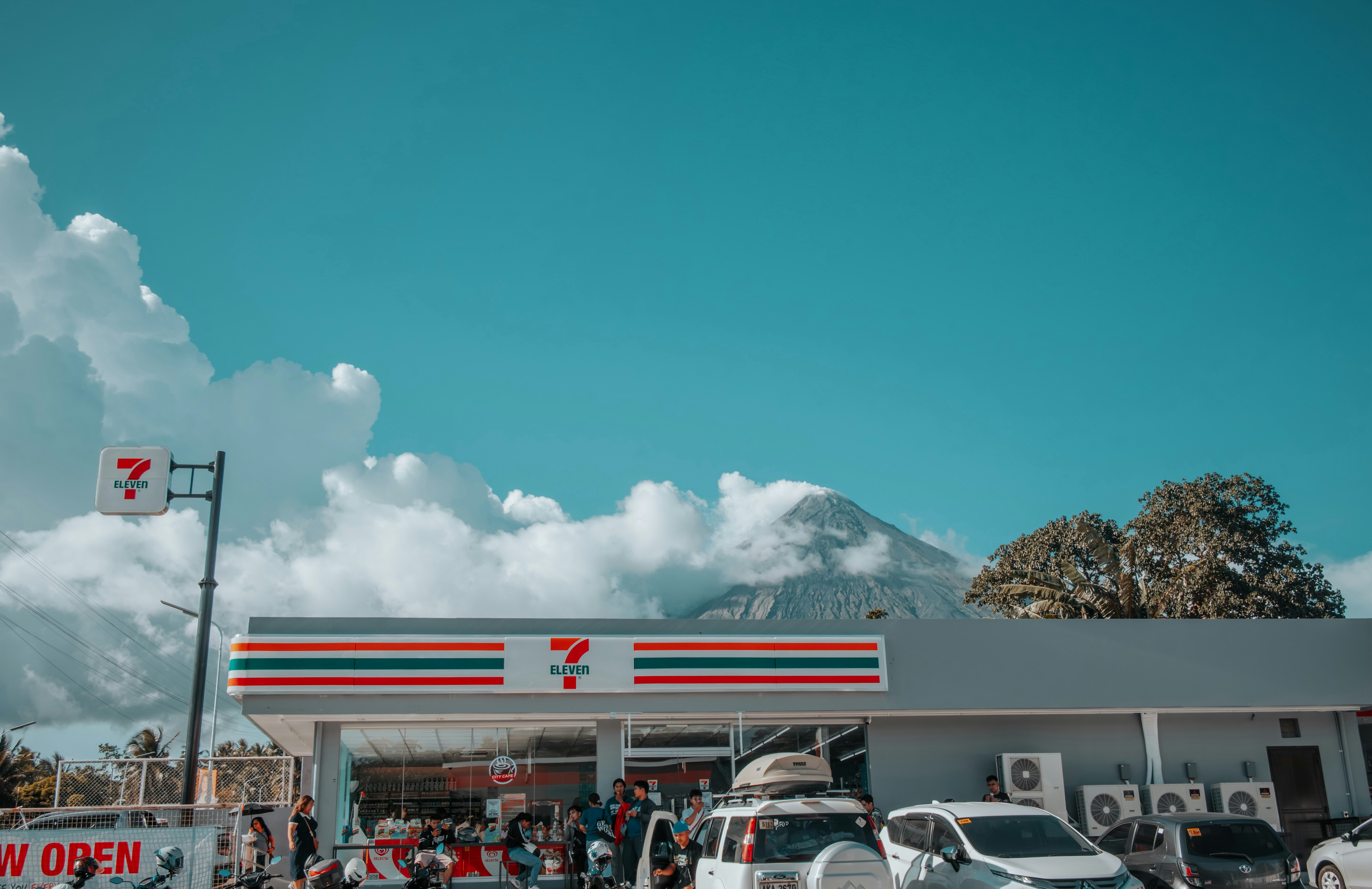 A vibrant convenience store bustling with customers, set against a backdrop of majestic mountains and a clear blue sky.