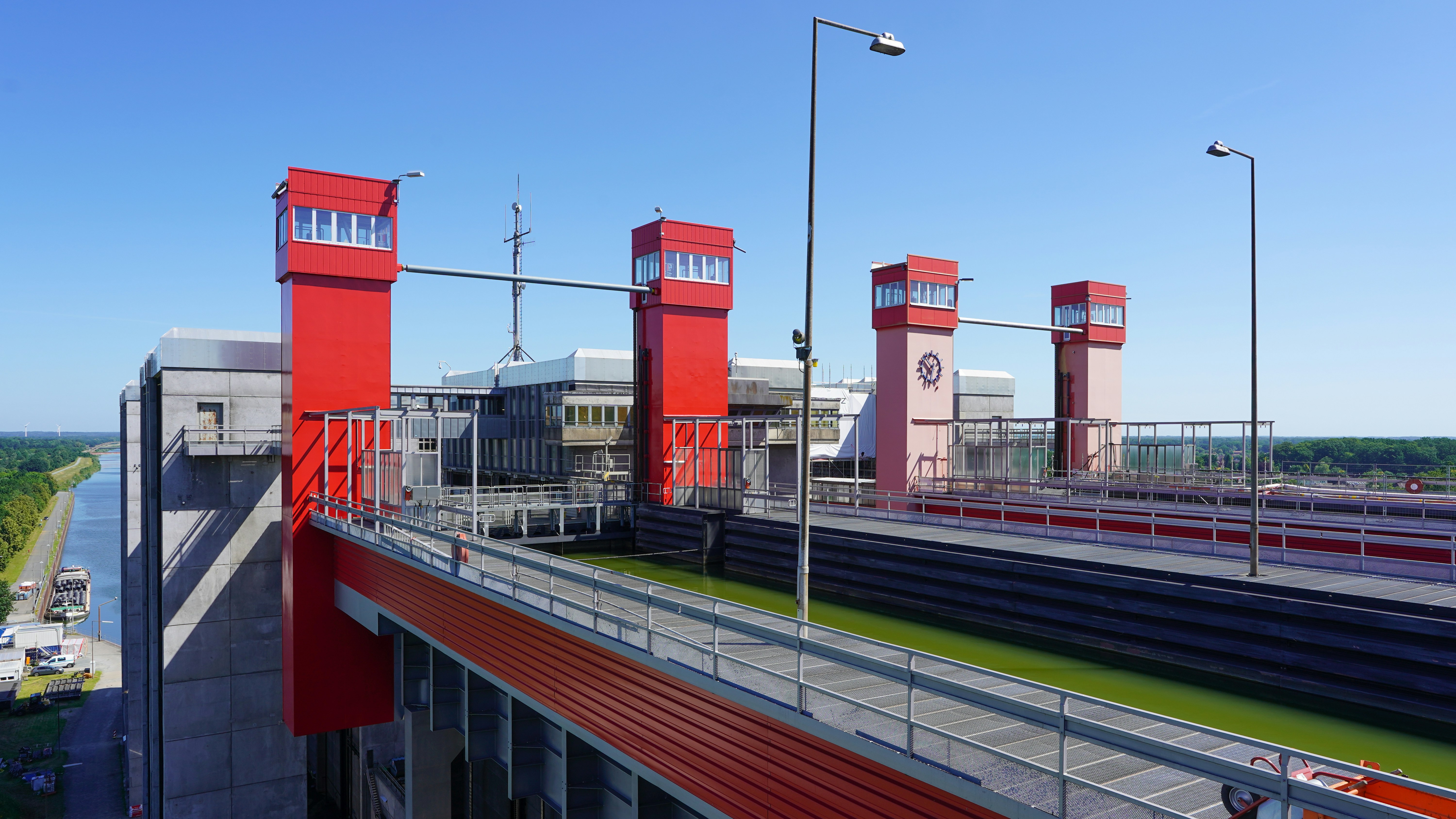 A vibrant hydraulic structure featuring bold red towers against a clear blue sky, showcasing modern engineering aesthetics. The scene captures a blend of functionality and design.