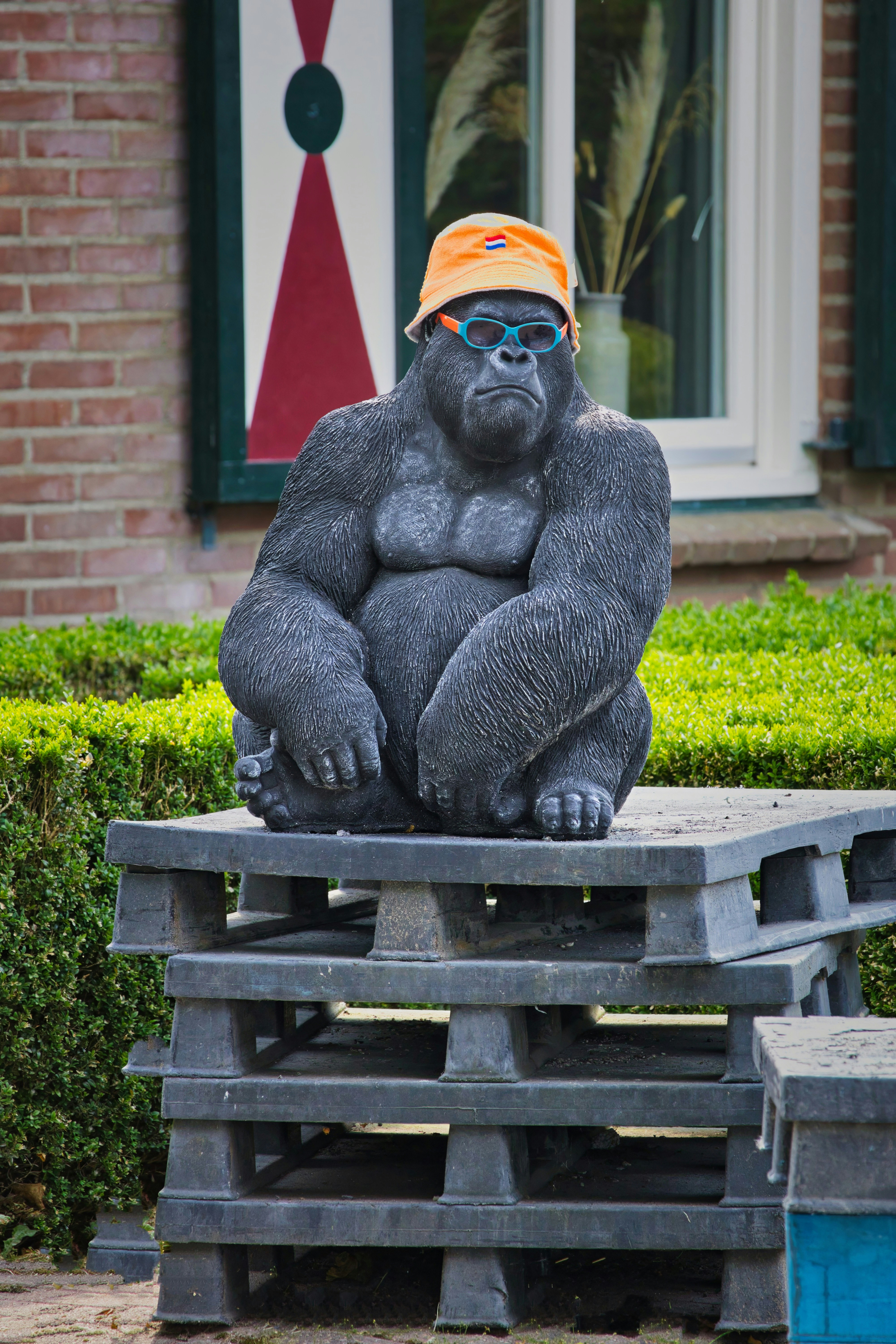 Orange-Bucket-Hatted Gorilla: A Stoic Statue on Pallet Stage