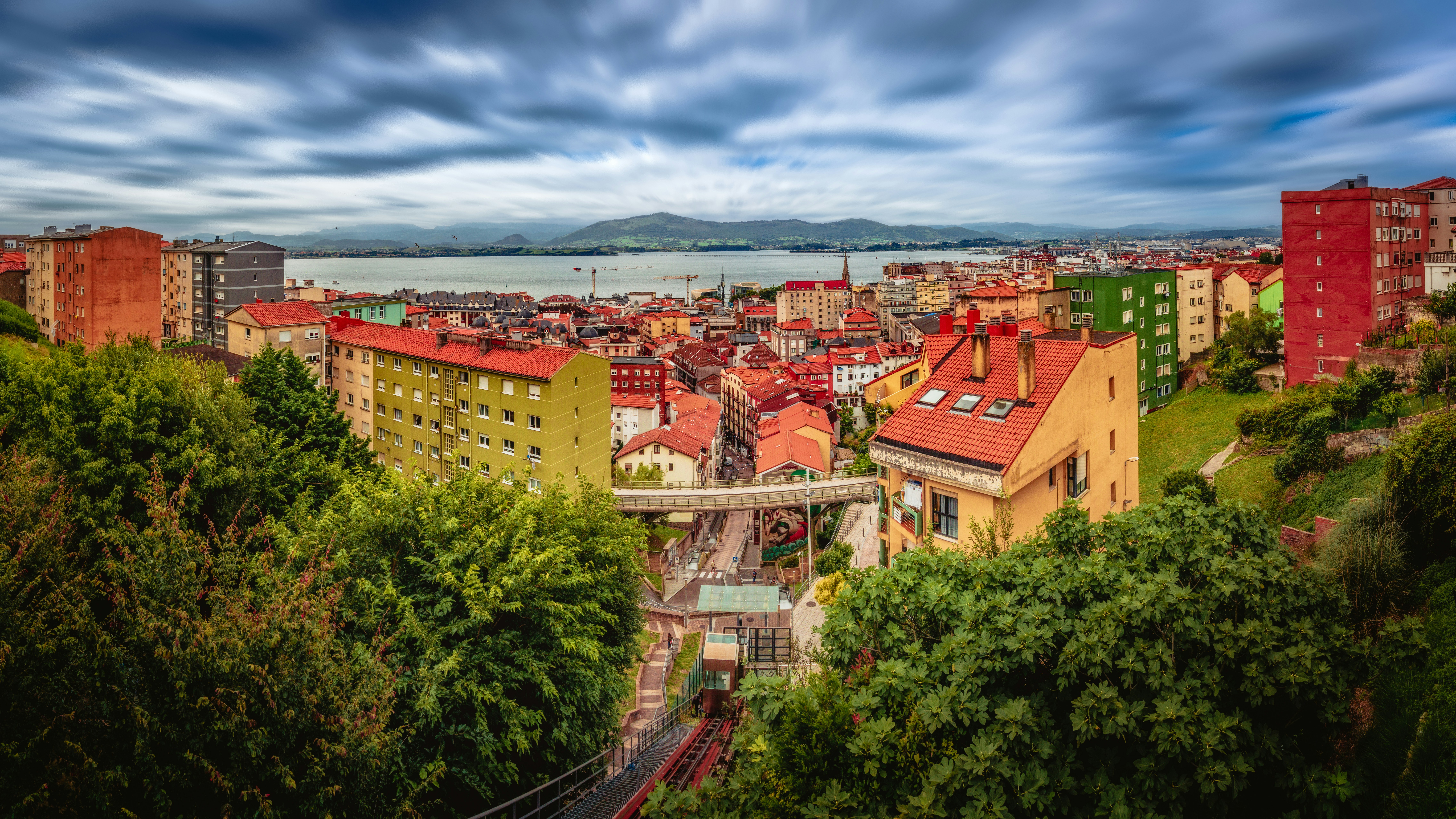 Vibrant cityscape showcasing a mix of colorful buildings and lush greenery, nestled against a serene coastal backdrop. A dynamic blend of urban life and nature.