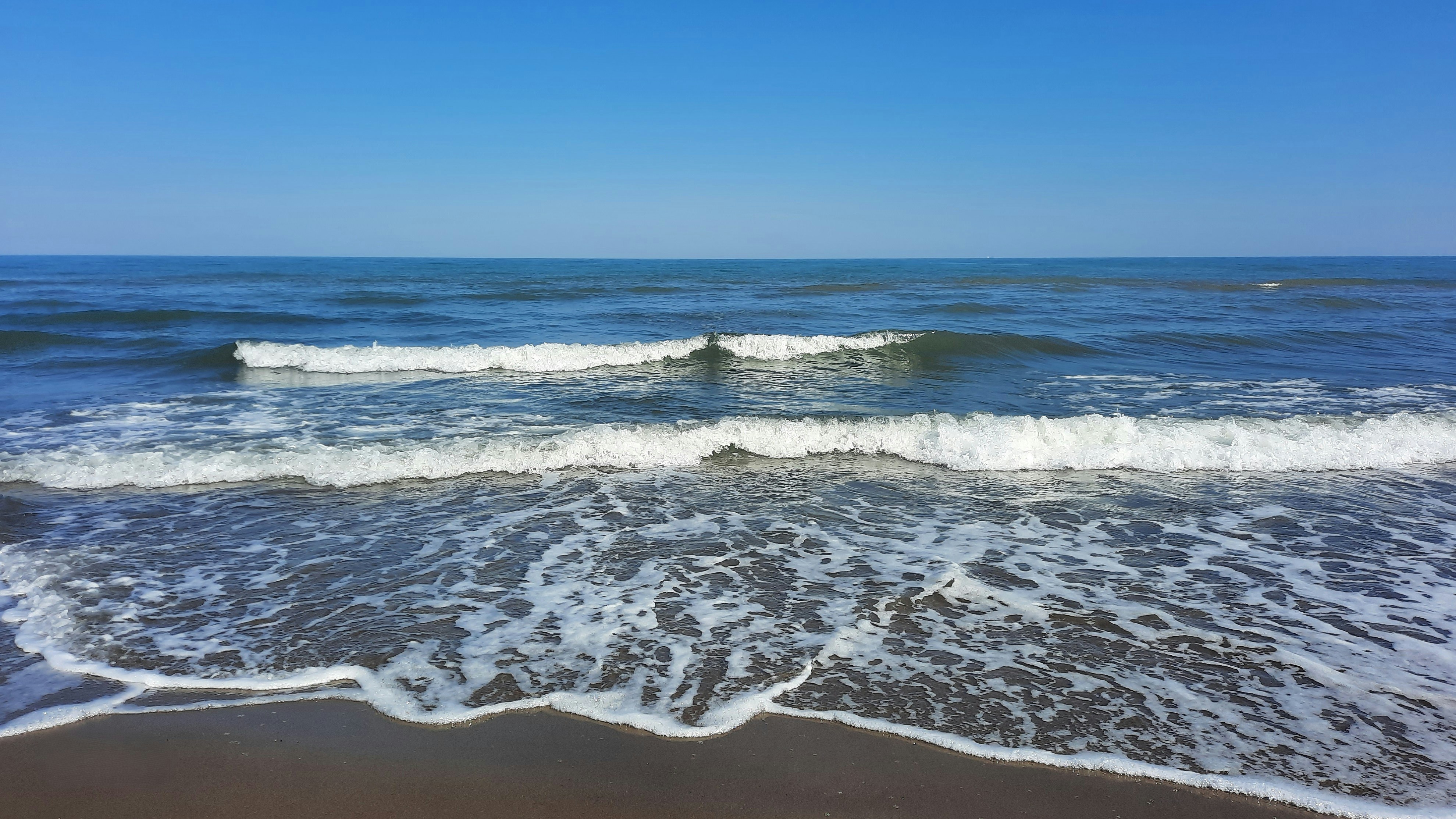 Gentle waves lapping at the shore under a clear blue sky, capturing the serene essence of a coastal landscape.