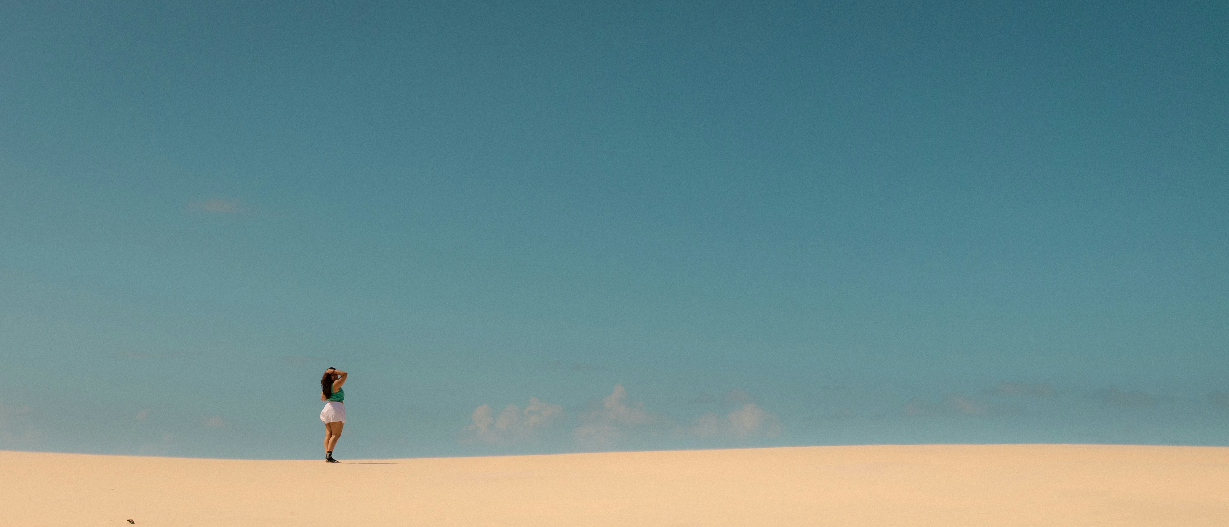 A lone figure stands on a vast sandy landscape under a clear blue sky, embodying a moment of introspection and peace.