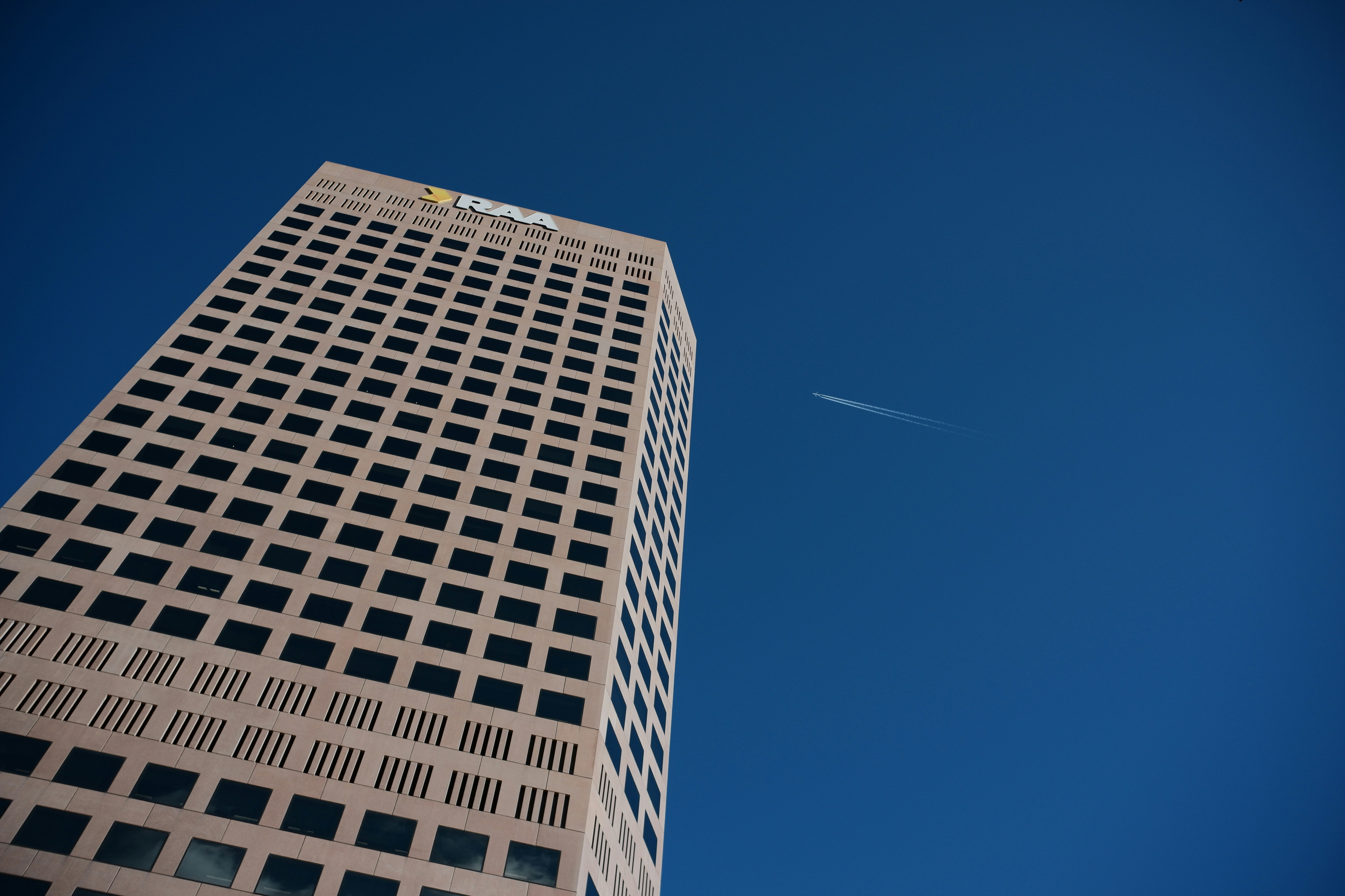 Tilted Facade Against a Cerulean Expanse: Skyscraper Meets Subtle Jet Trail