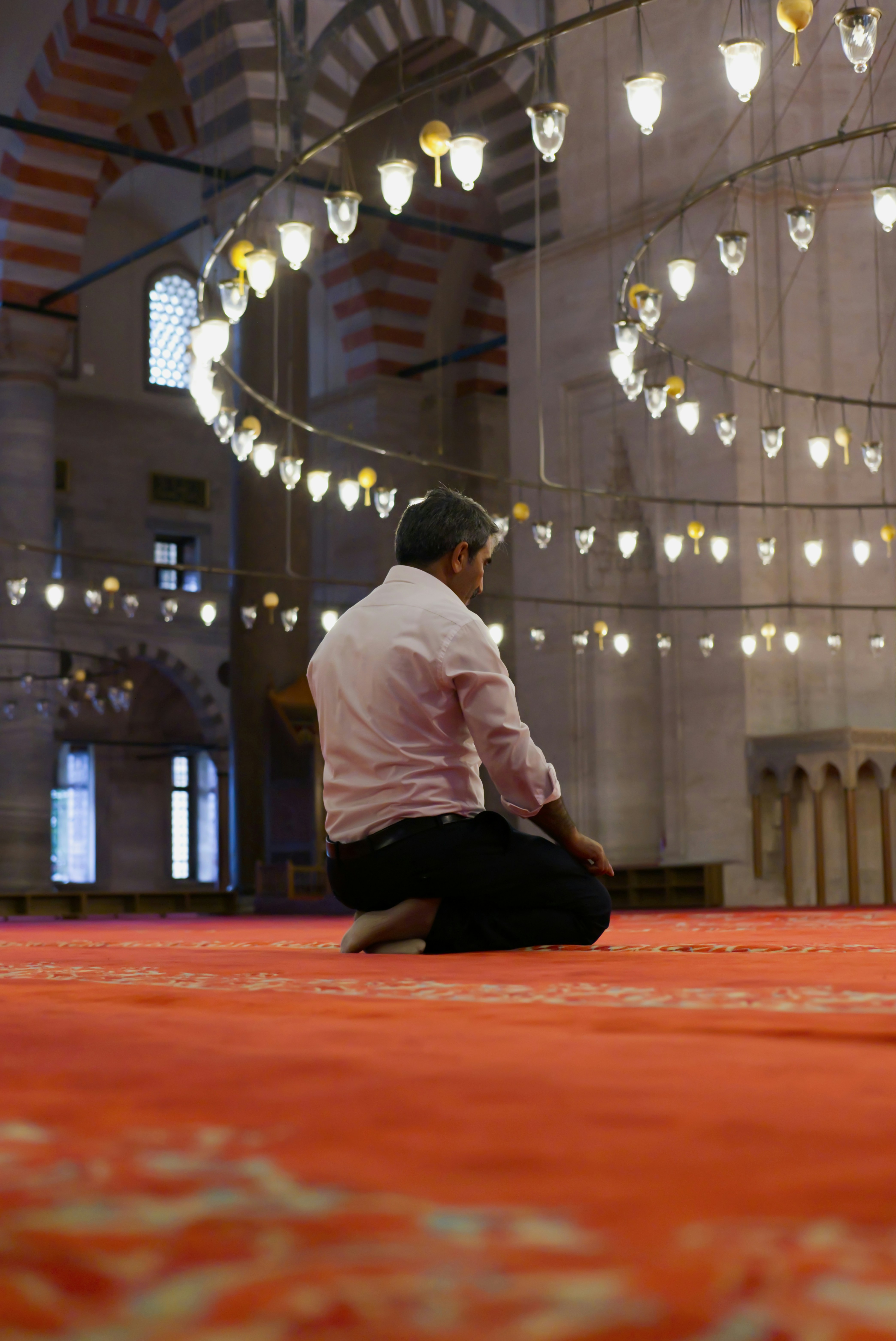 A man prays on a mosque's red carpet.