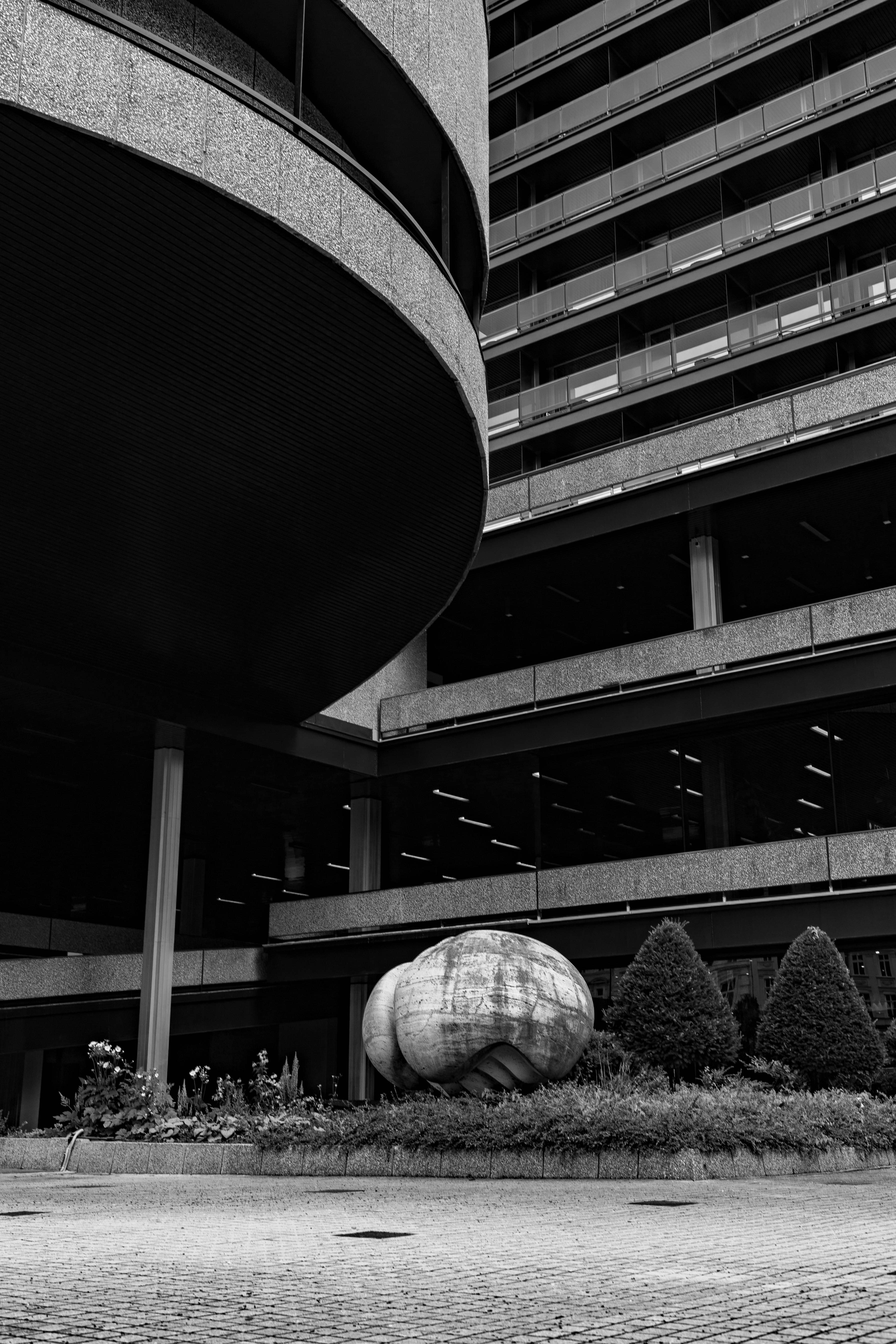 Abstract sculpture nestled among greenery at the base of a modern building, showcasing a blend of natural and urban elements.