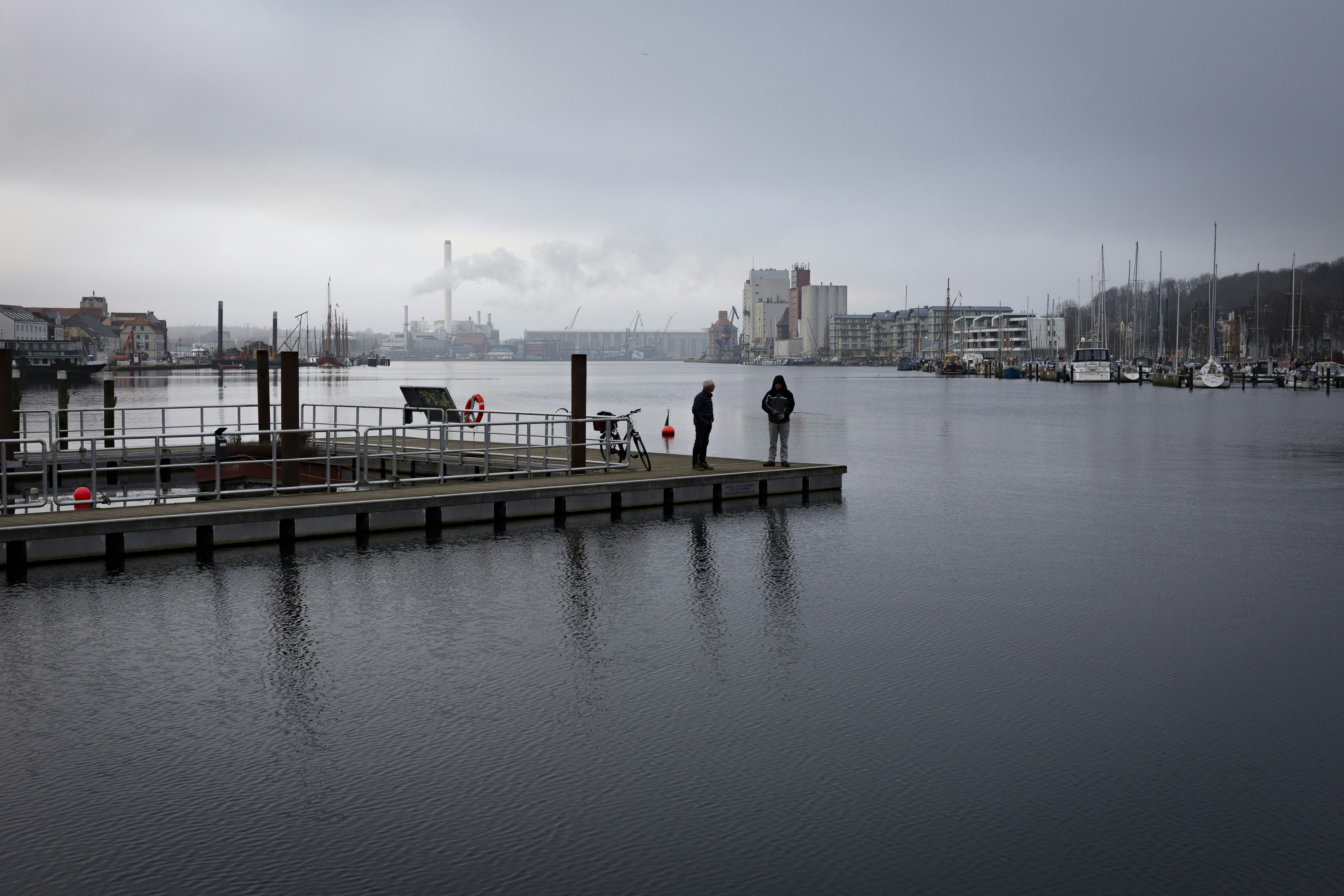 Two people fish on a pier in overcast weather.