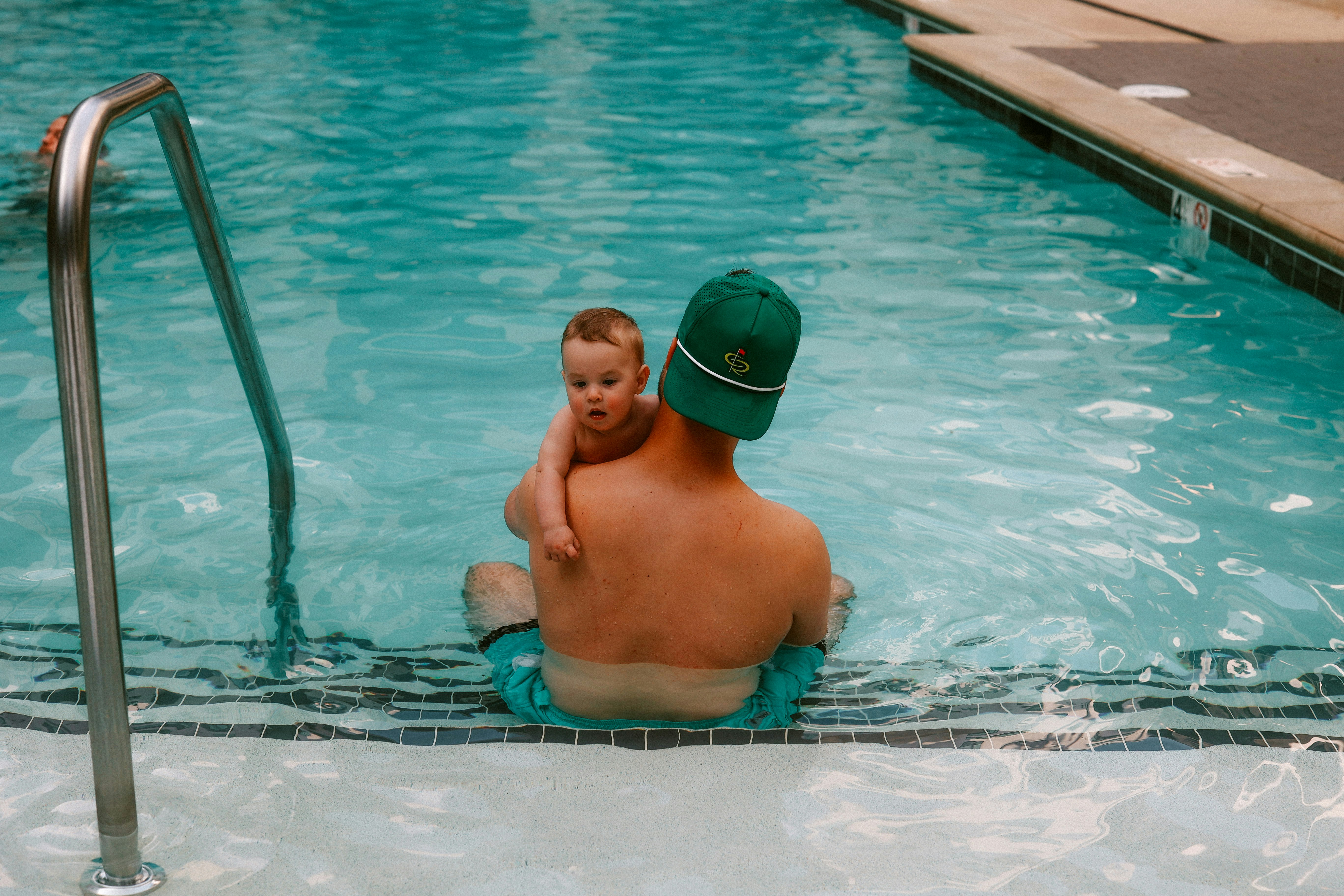 Man holding a baby in a swimming pool, enjoying a tranquil moment together. The soft ripples of water create a calming backdrop.