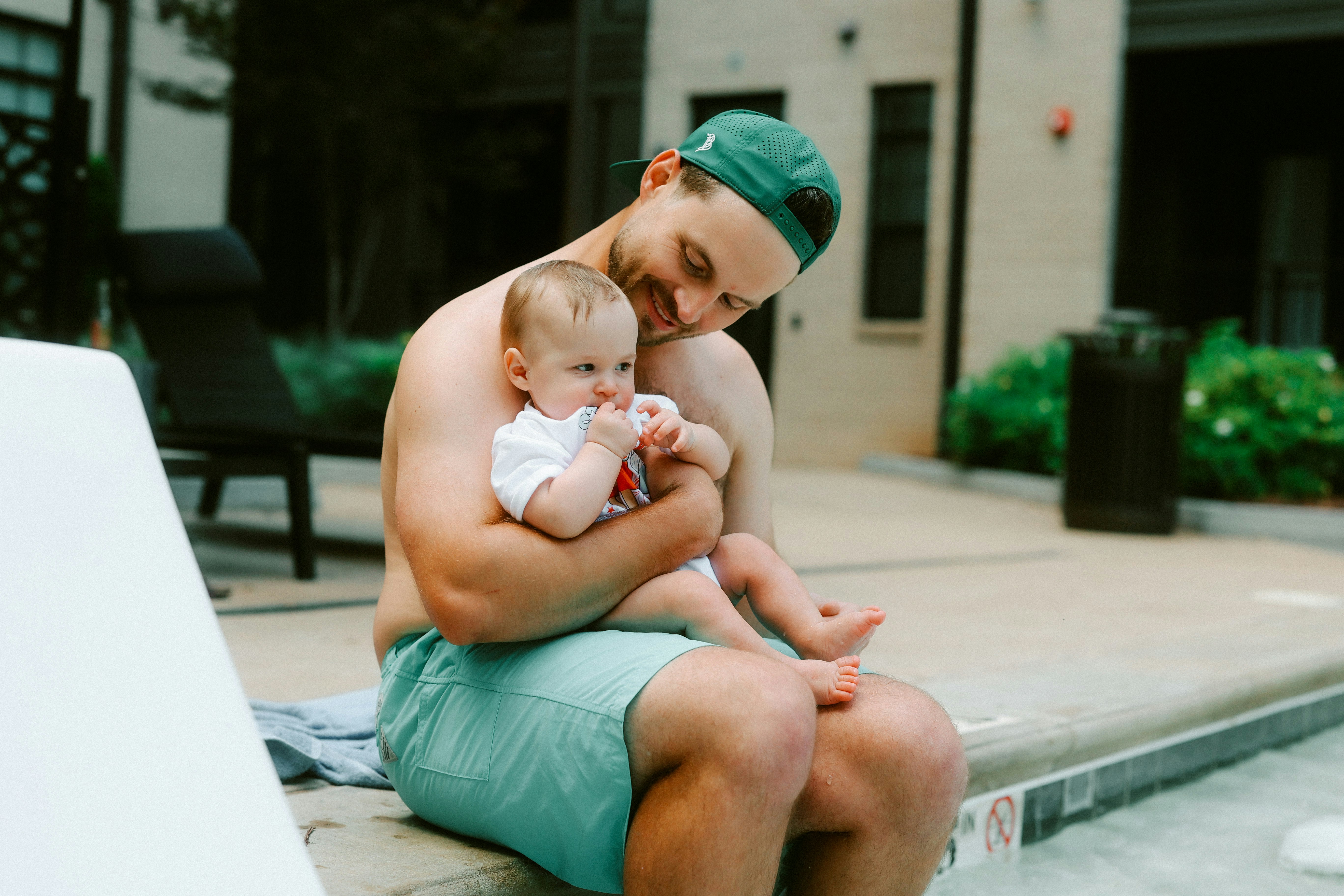 A father lovingly cradles his baby by the poolside, embodying a serene moment of connection. The scene captures the warmth of family life in a relaxed outdoor setting.