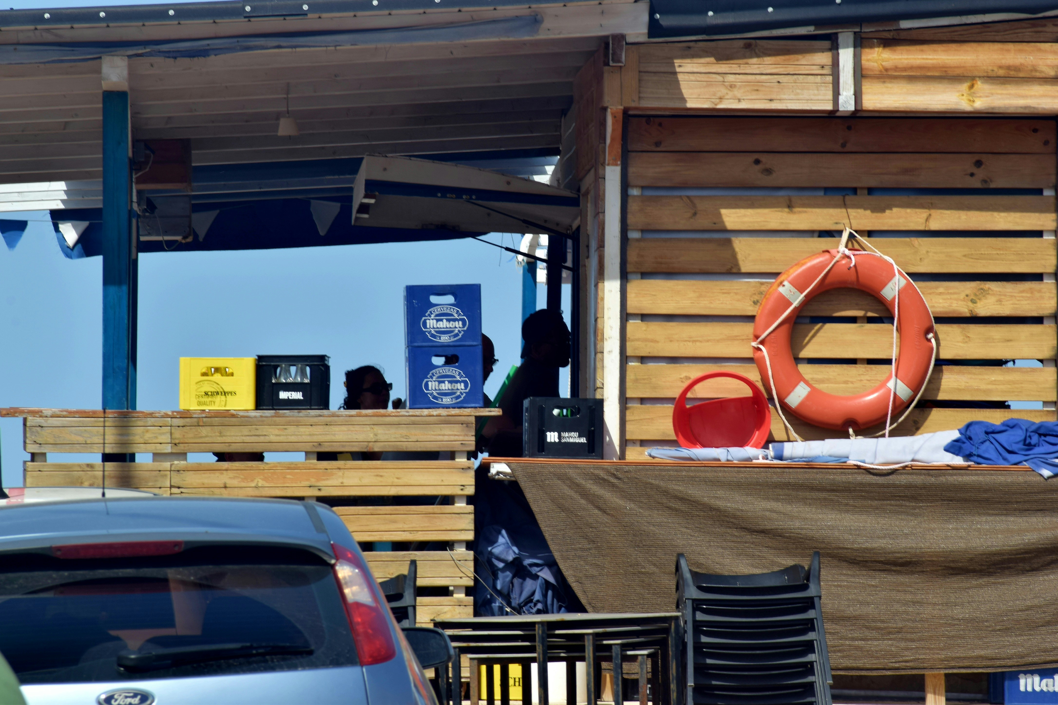 Vibrant beachside shack showcasing colorful signage and a lifebuoy, with patrons enjoying the atmosphere. The wooden structure adds rustic charm.