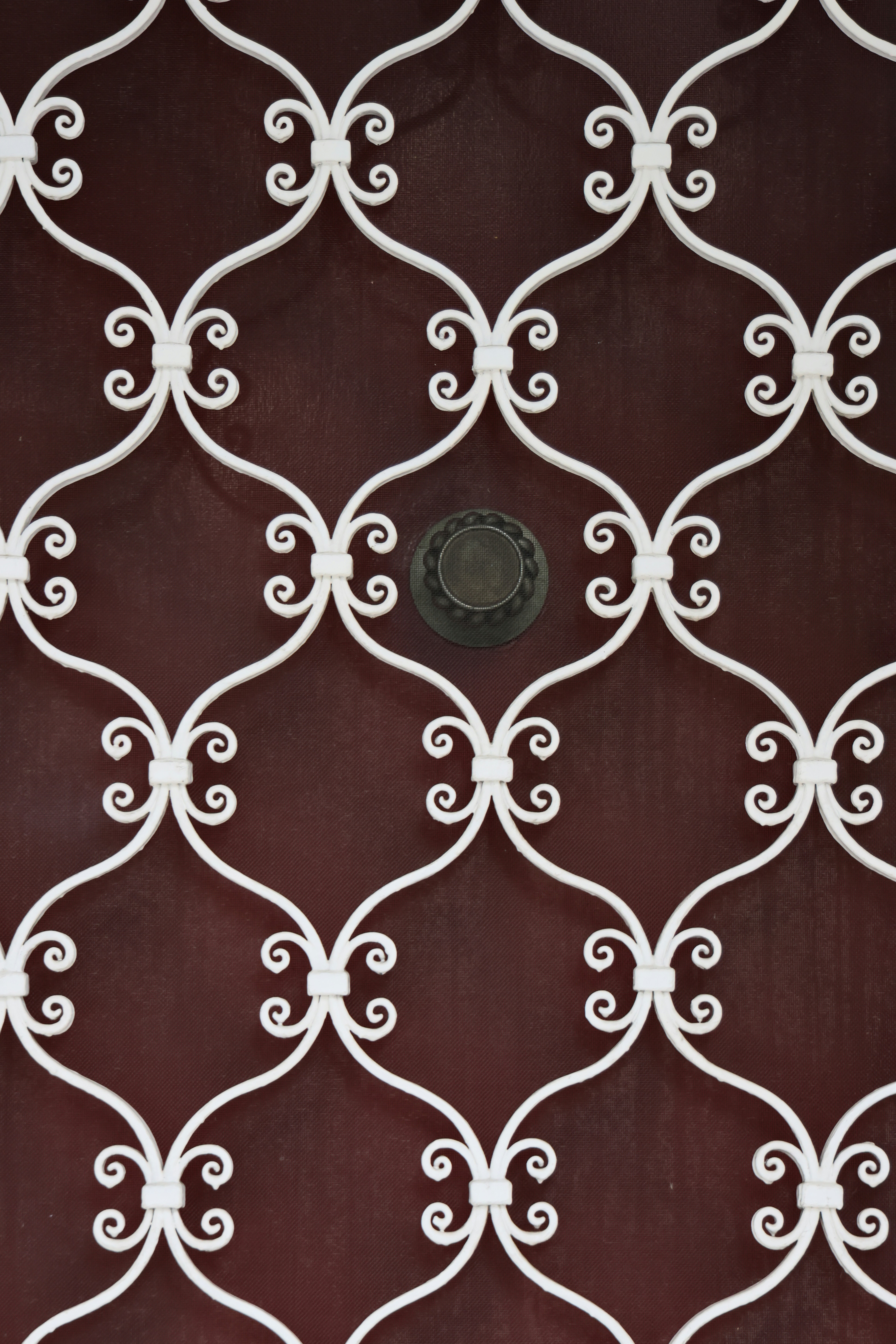 Decorative ironwork on a maroon background, featuring a central circular element amidst a swirling pattern. The design showcases craftsmanship and attention to detail.