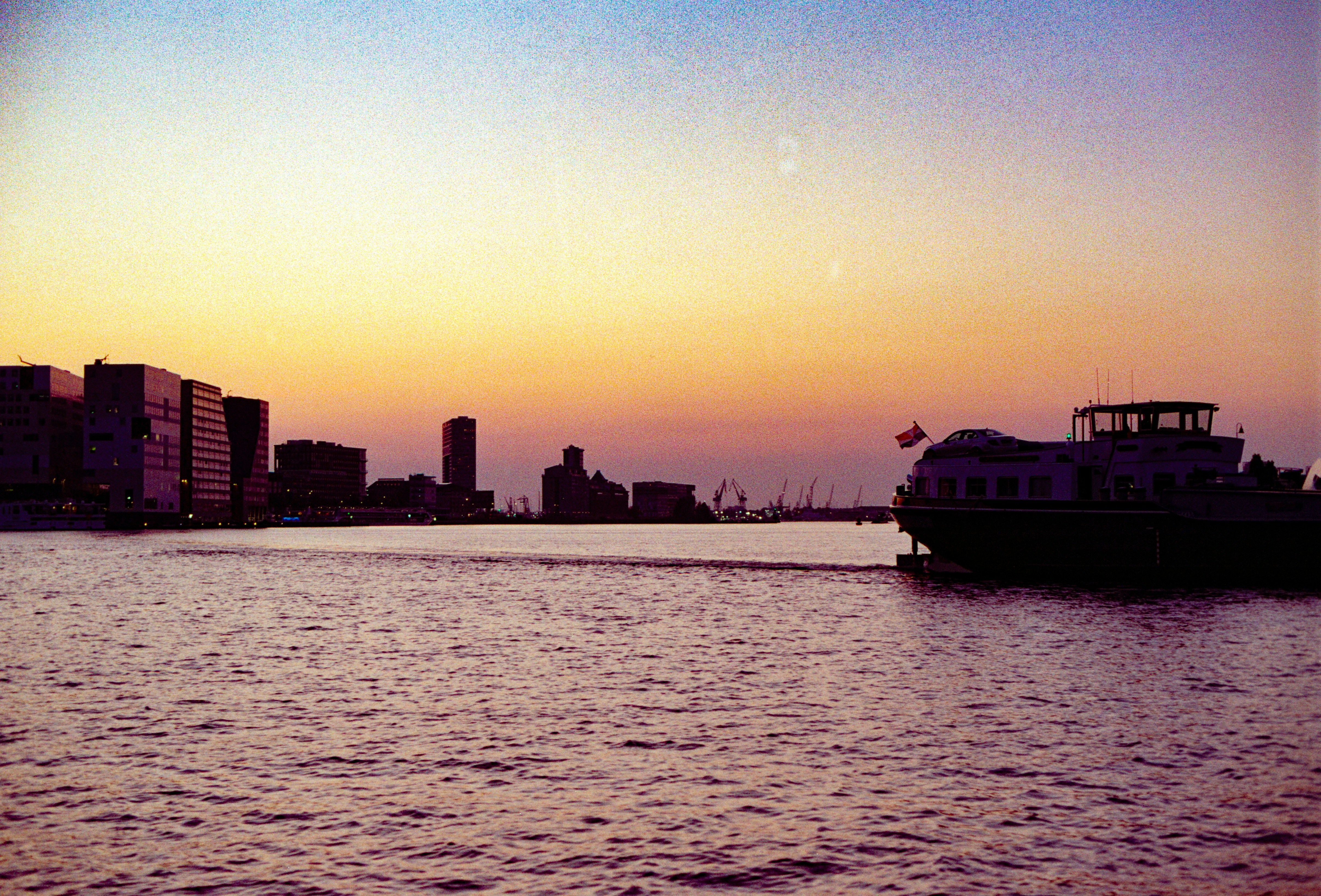 Silhouetted skyline at dusk with a boat gliding across the shimmering water, capturing the transition from day to night.