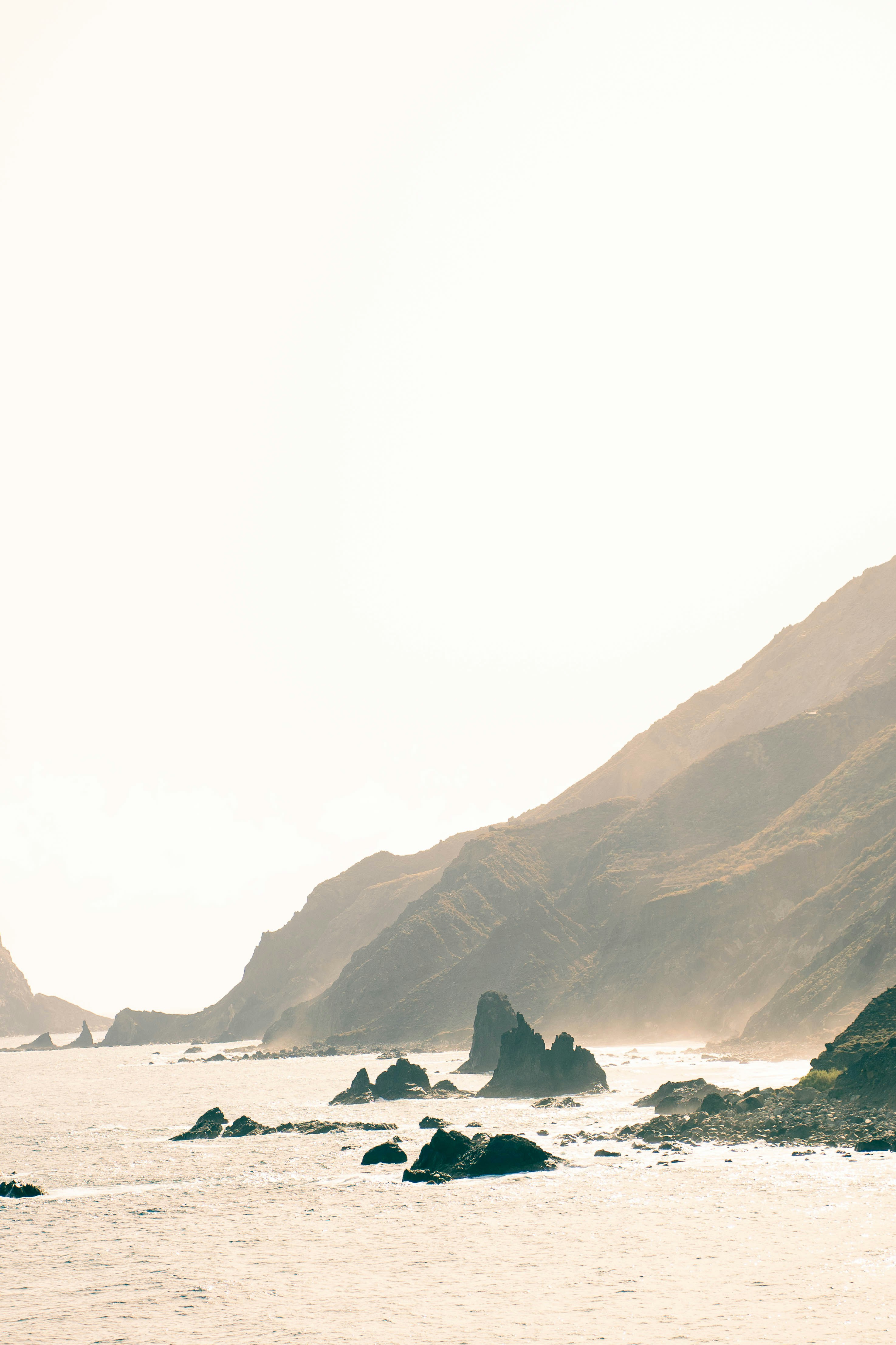 Softly illuminated coastline with rugged rocks jutting into the ocean, enveloped in a gentle haze.