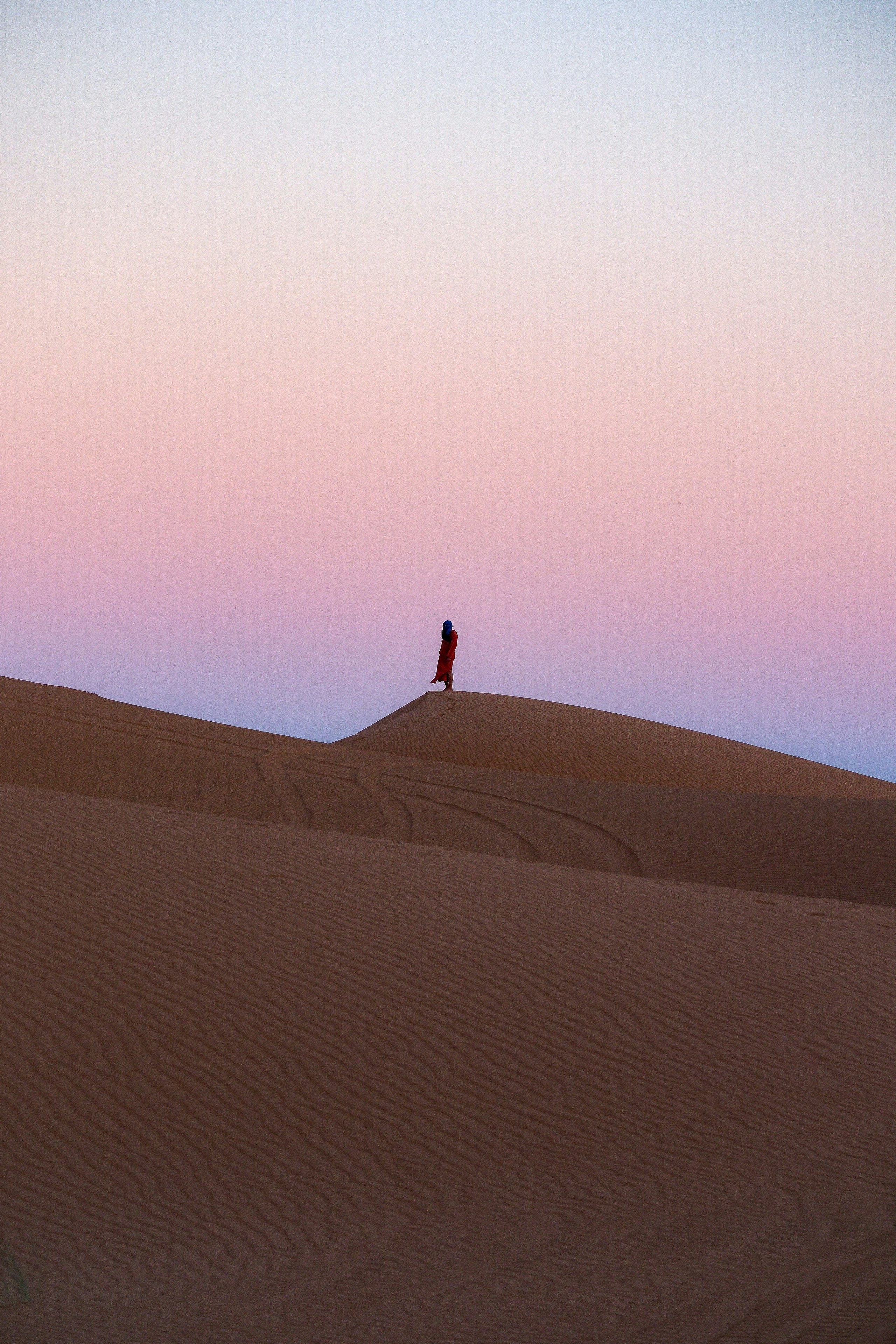 A person stands on a desert dune at sunset.