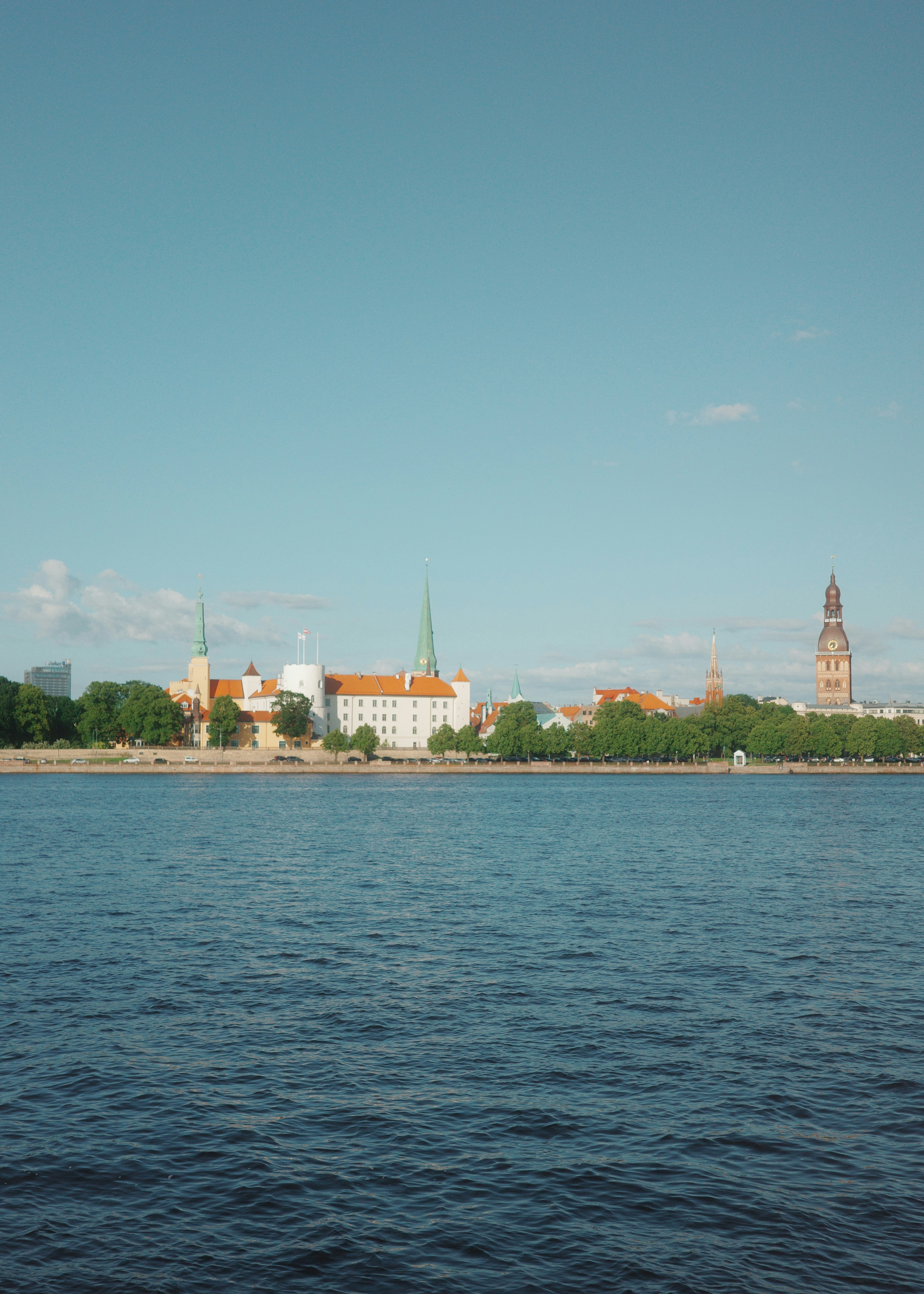 Historic skyline featuring a blend of spires and modern structures along a tranquil waterfront. The scene captures the essence of city life by the river.
