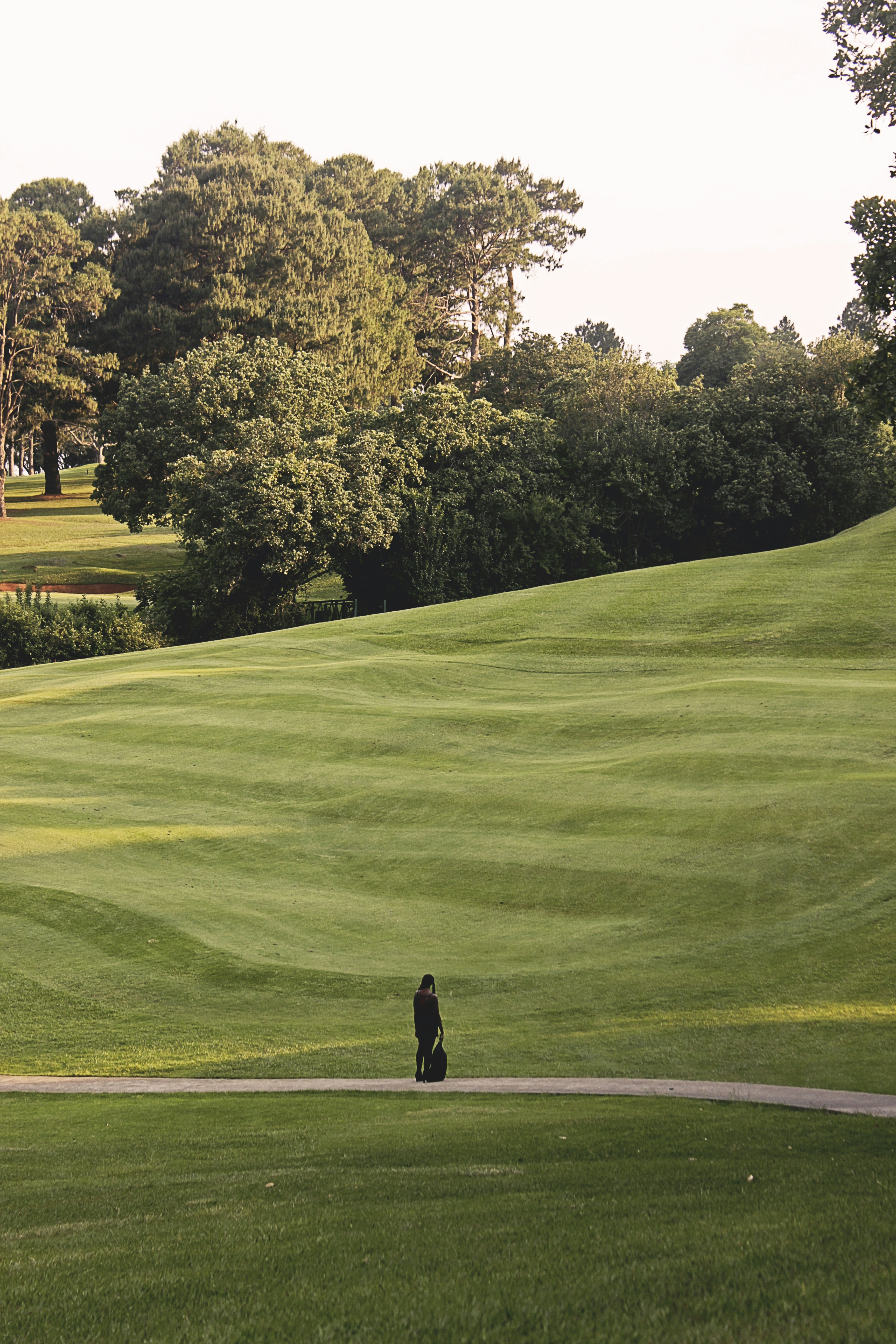 Person standing grass field | A person walks alone on a lush green golf course.