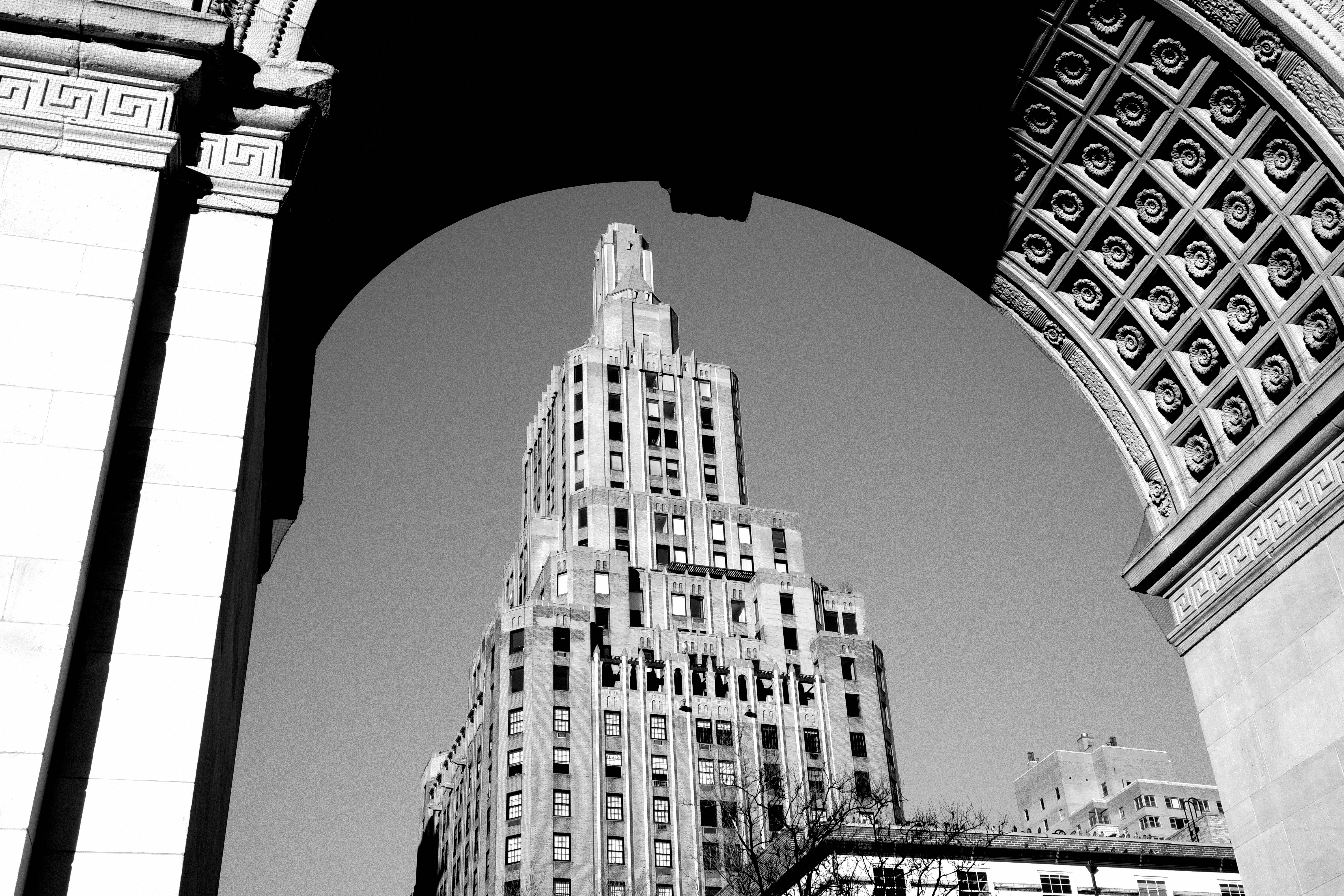 Art Deco skyscraper viewed through an ornate archway, highlighting the contrast between historic architecture and modern city life.