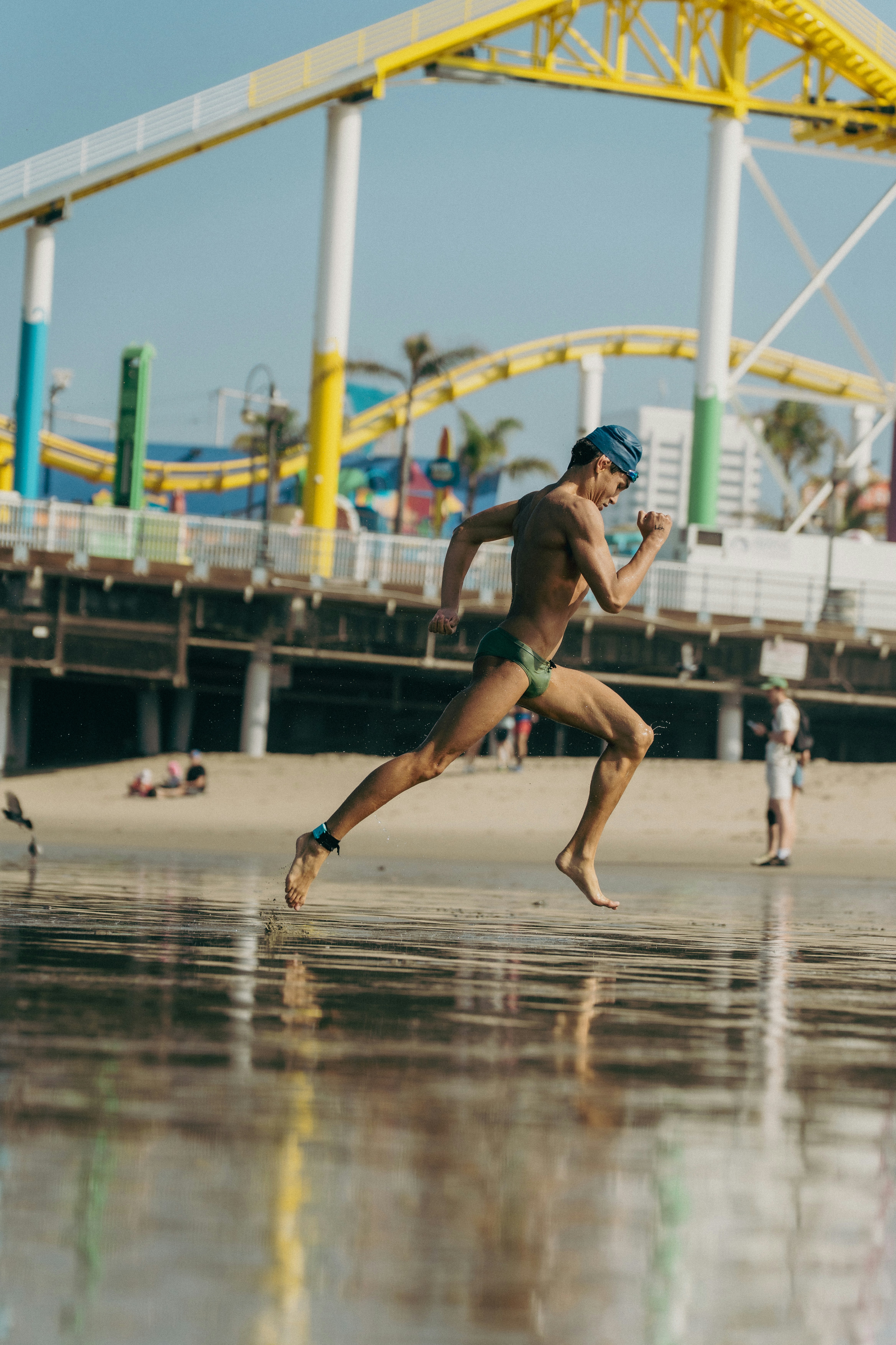 Athlete sprinting along the beach, creating splashes in the shallow water with a vibrant amusement park in the background.