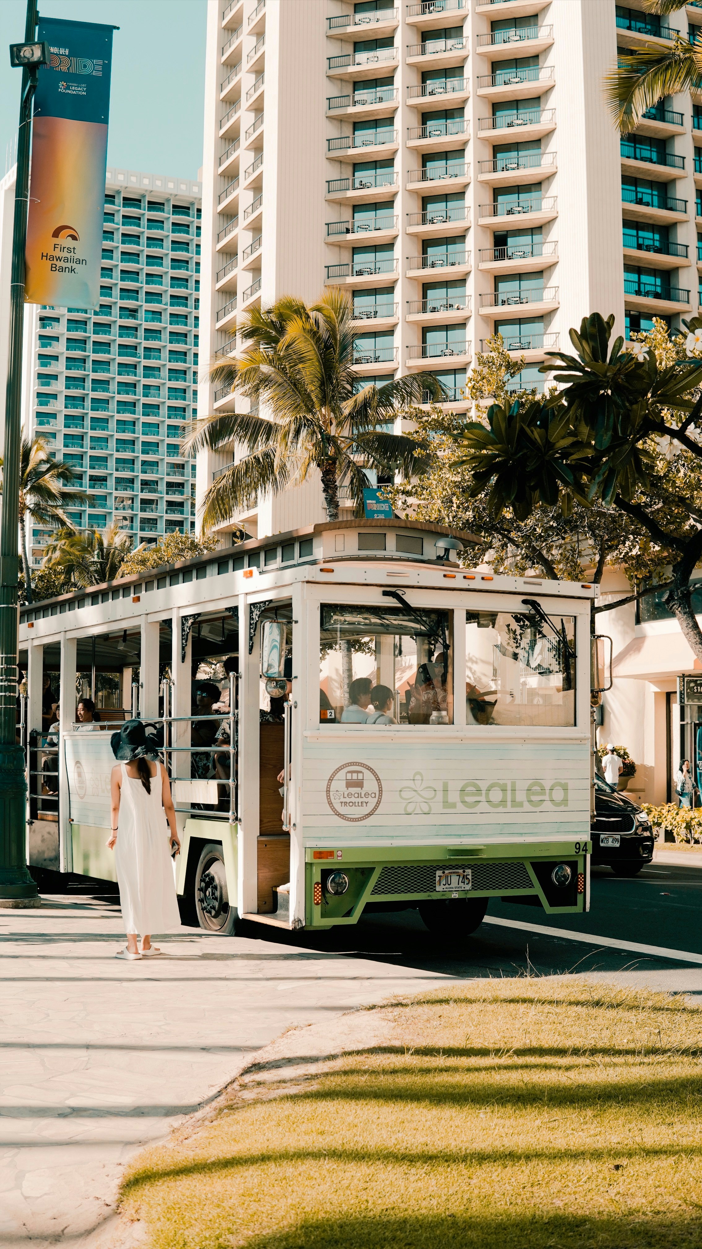 Lealea shuttle pausing under sunlit high-rises amid palm-lined streets