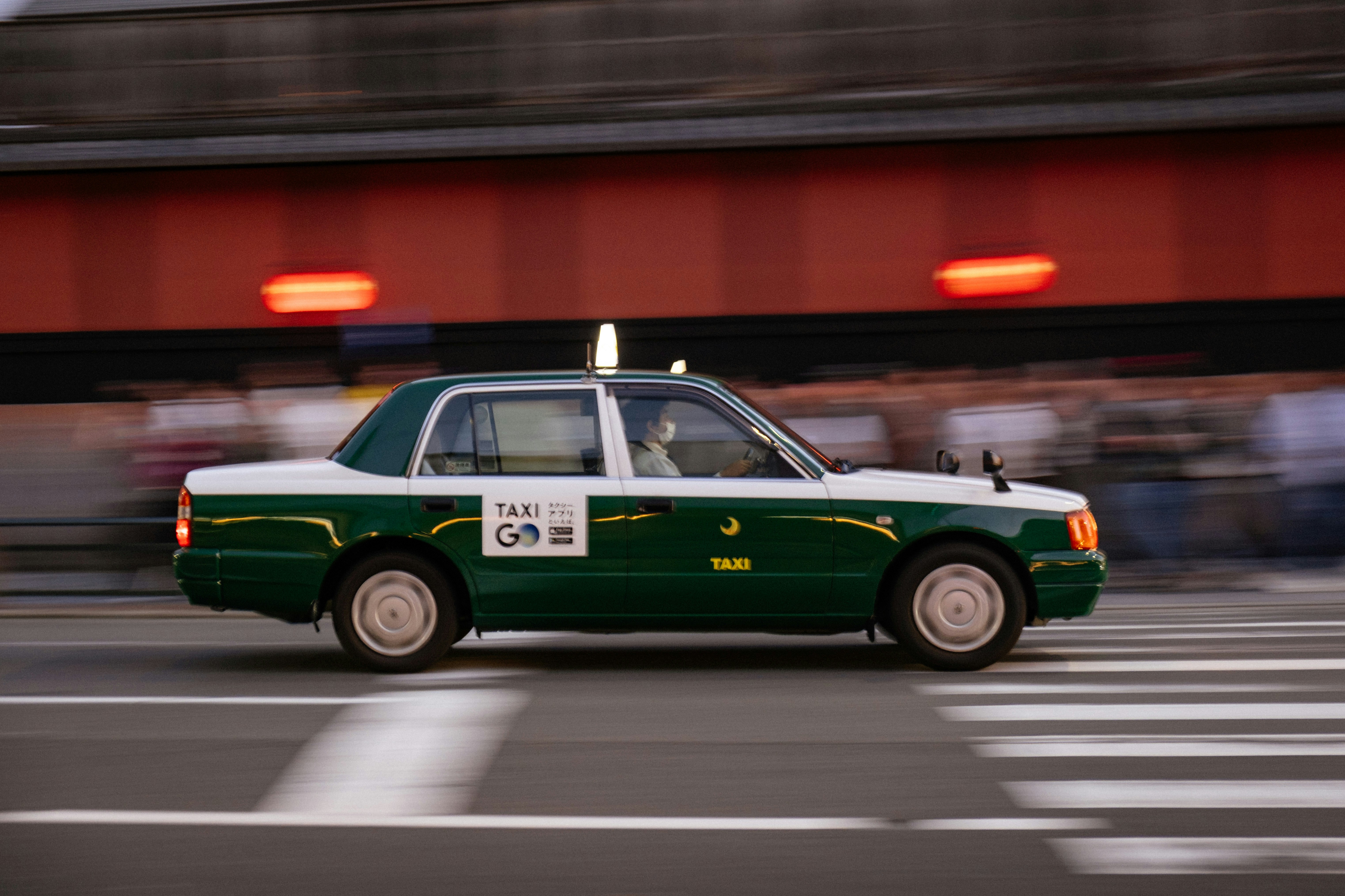A green and white taxi speeds through a bustling city street, with blurred pedestrians and lights in the background, conveying a sense of motion and urban life.