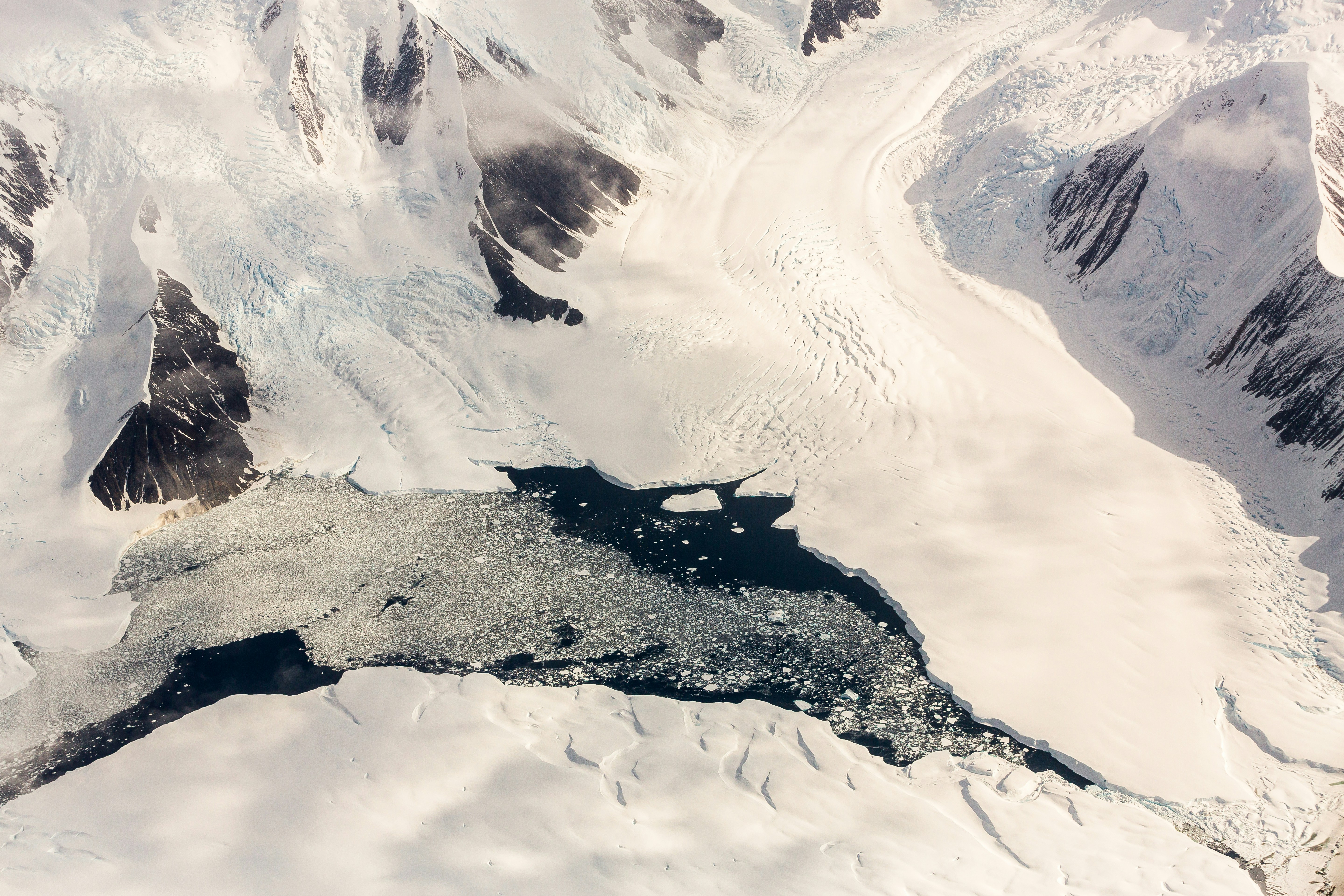 Aerial view of a glacial landscape featuring a dark water body surrounded by ice and snow, highlighting the stark contrast between the elements.