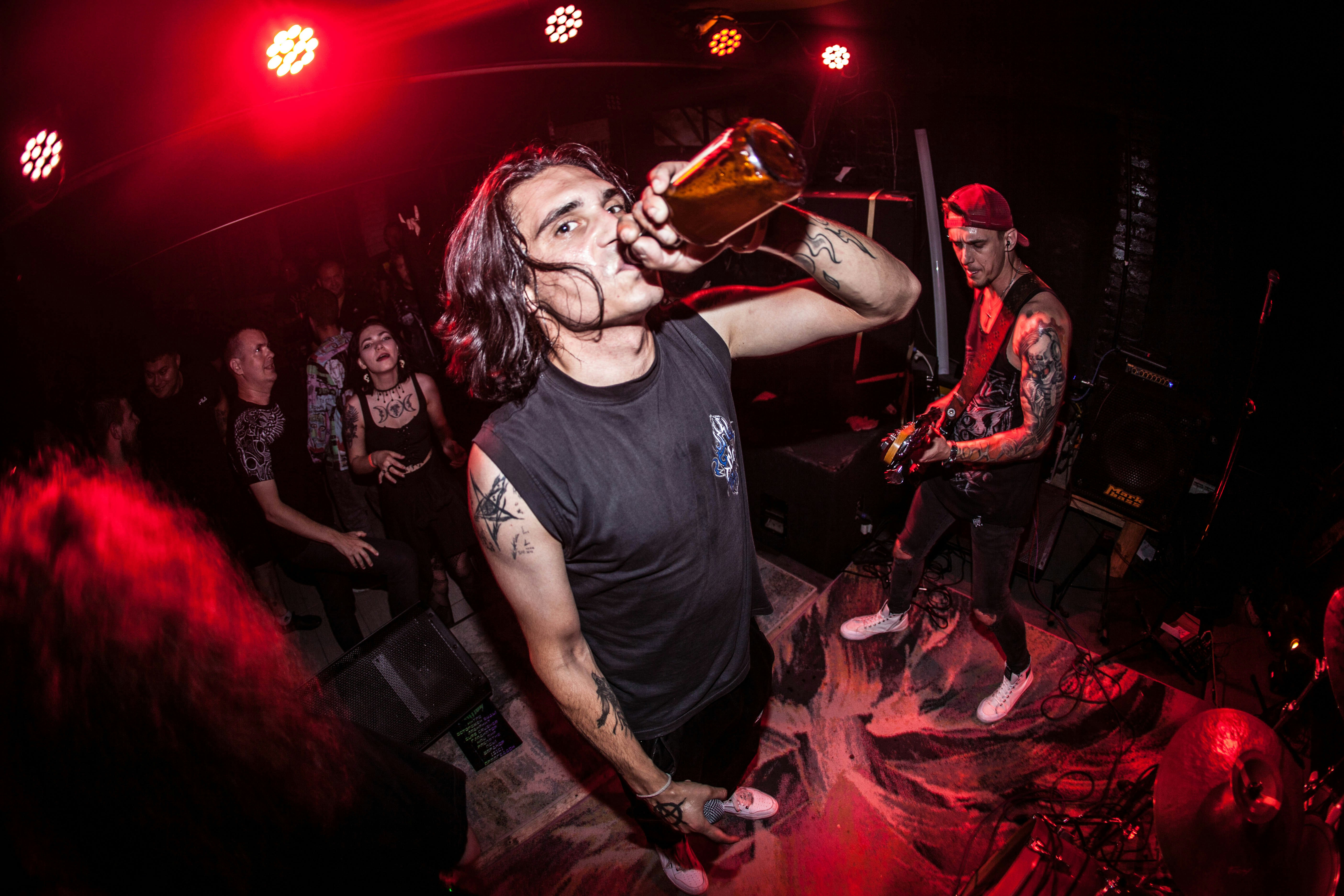 A man drinks beer while rock band plays.