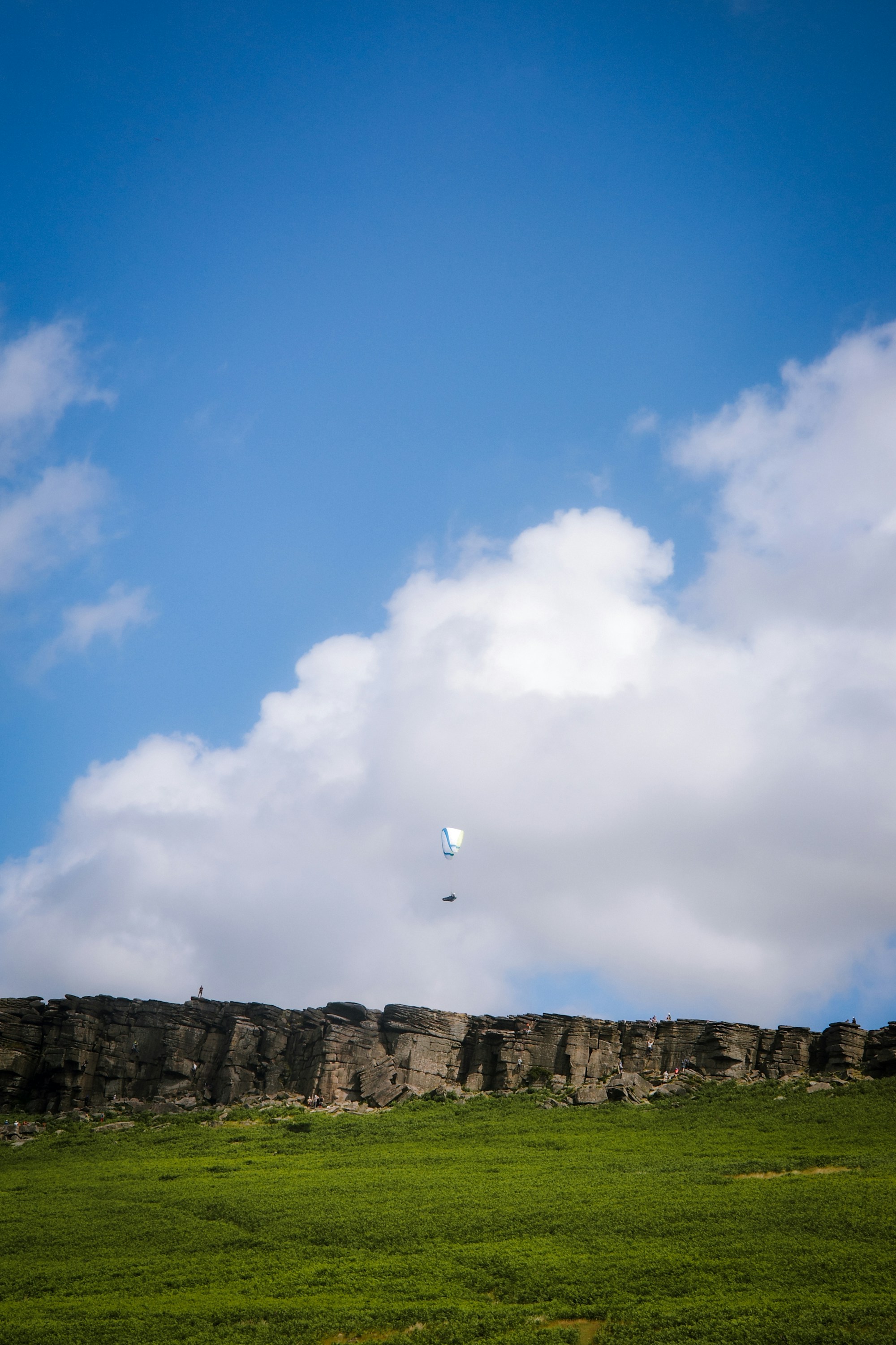 Aerial Quiet: Paraglider Over a Rugged Cliff and Lush Plain