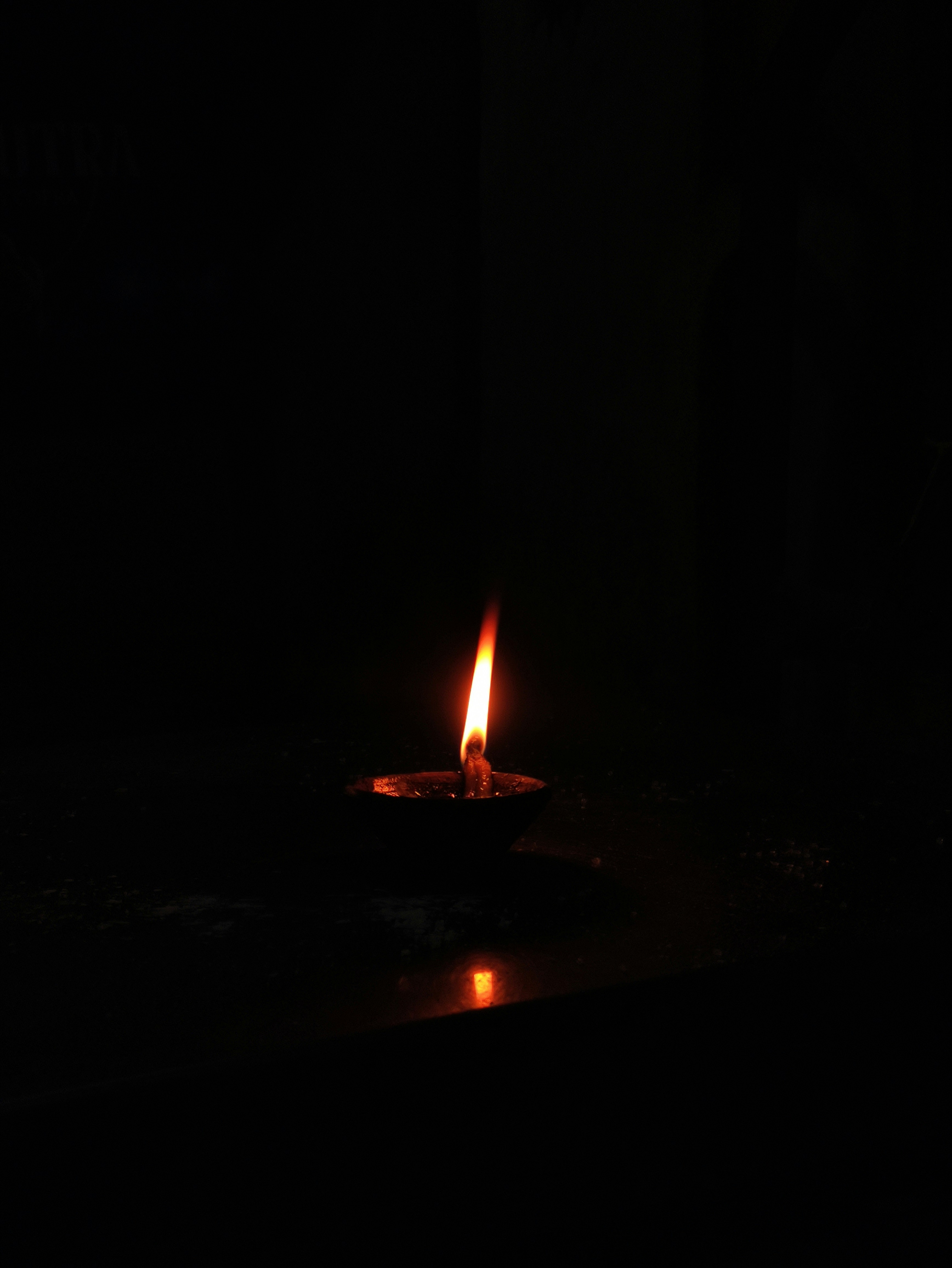 A lit candle shines brightly in darkness.