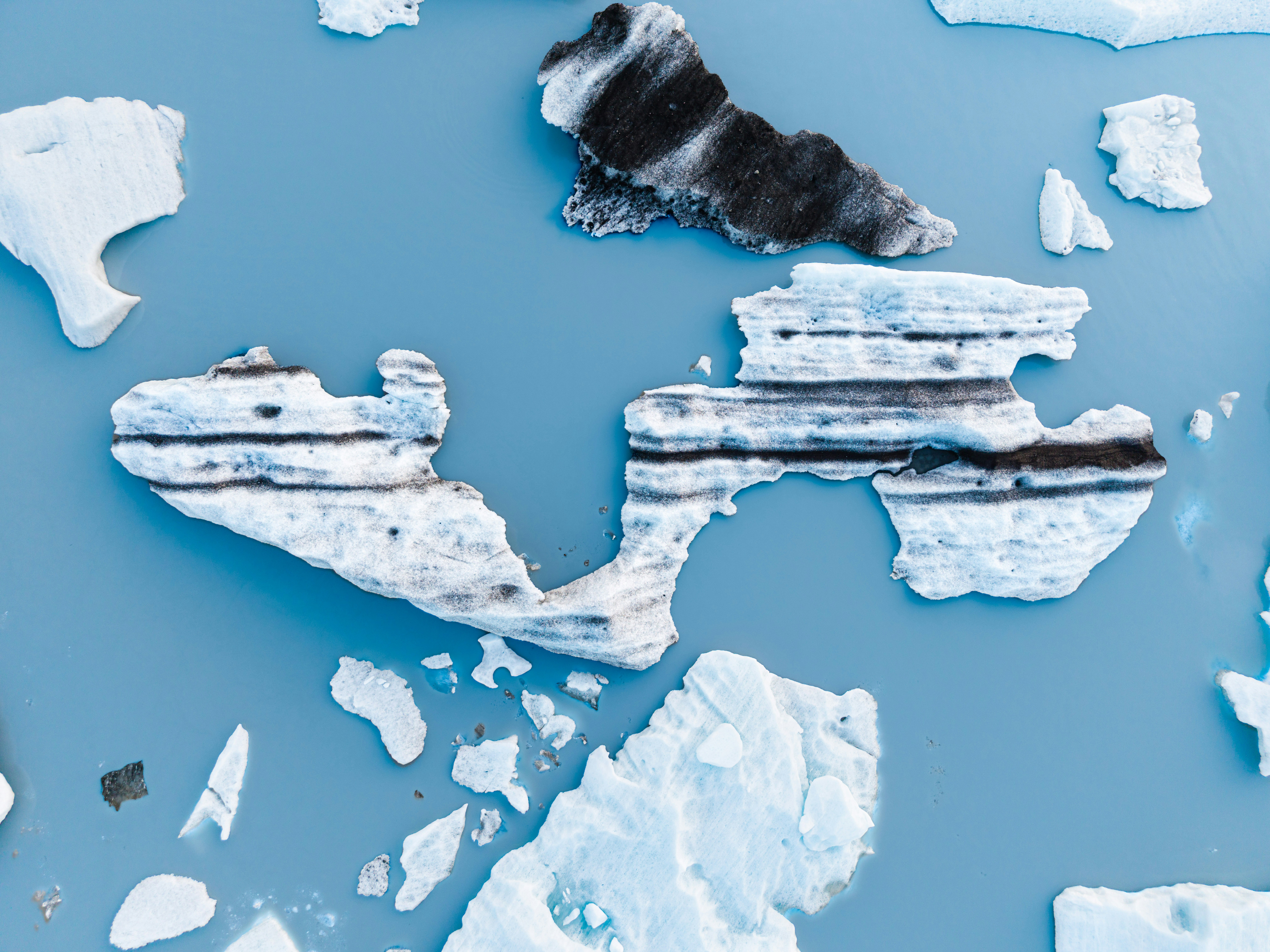 Intricate ice formations float atop a serene blue expanse, showcasing a mix of textures and colors. The scene highlights the delicate balance of nature's artistry.