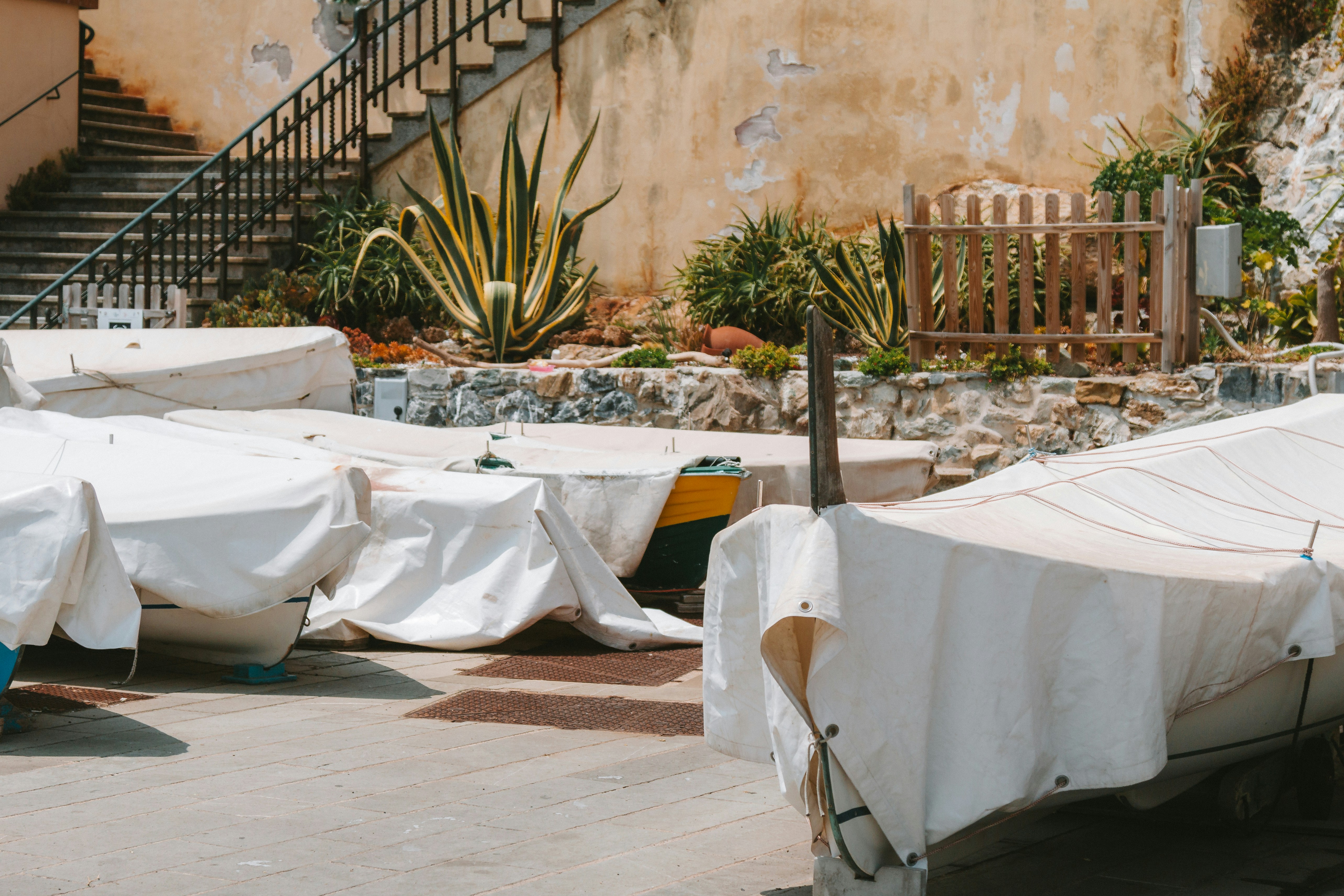 Boats covered with tarps resting in a serene harbor, surrounded by lush greenery and rustic architecture.