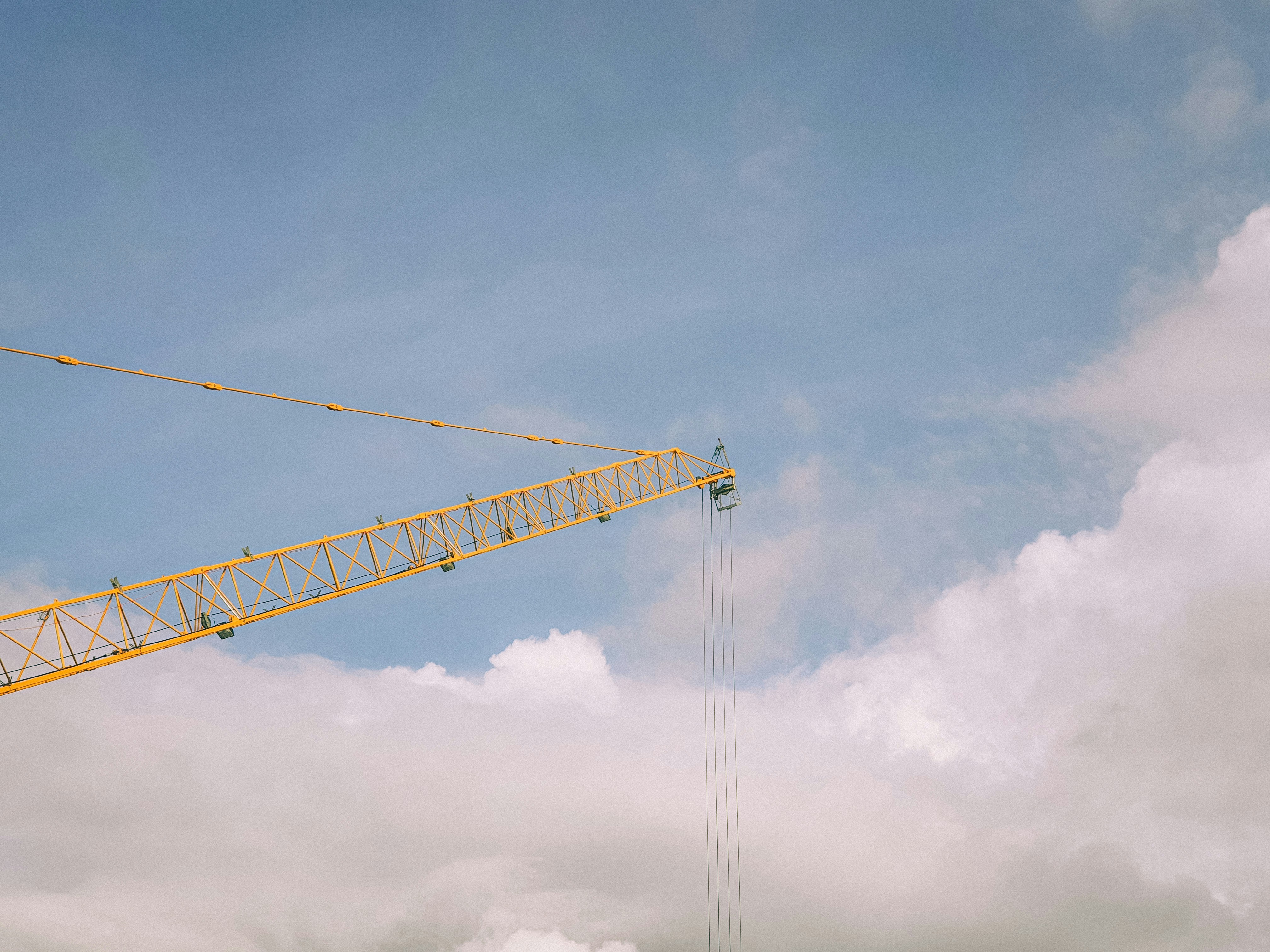 crane | Crane arm against a cloudy, blue sky.