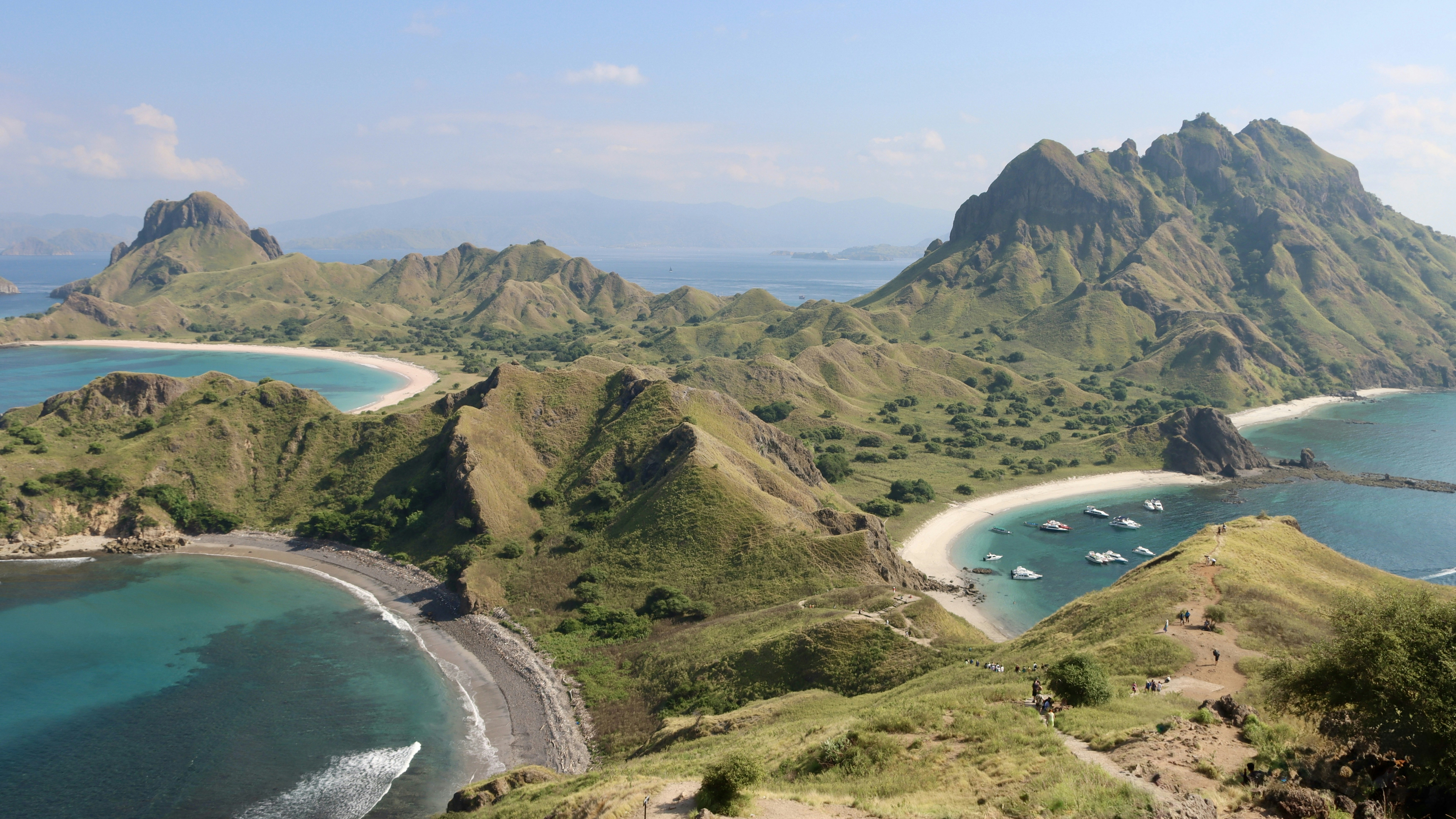 Vibrant coastal landscape showcasing lush green hills and tranquil blue waters, with boats anchored in the bay. The scene captures the harmony between land and sea.