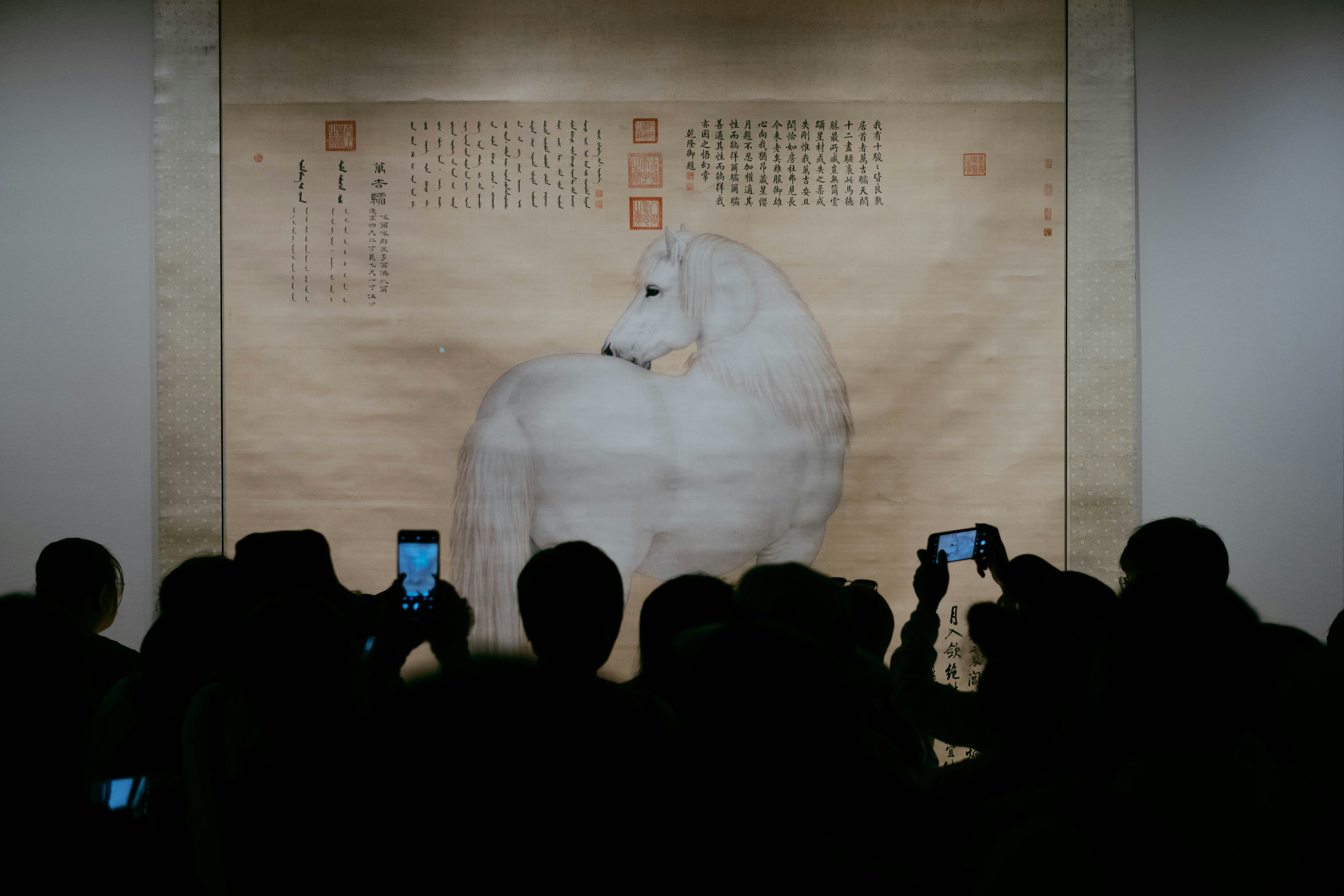 A majestic white horse stands in profile against a backdrop of traditional calligraphy, surrounded by silhouettes of onlookers capturing the moment.