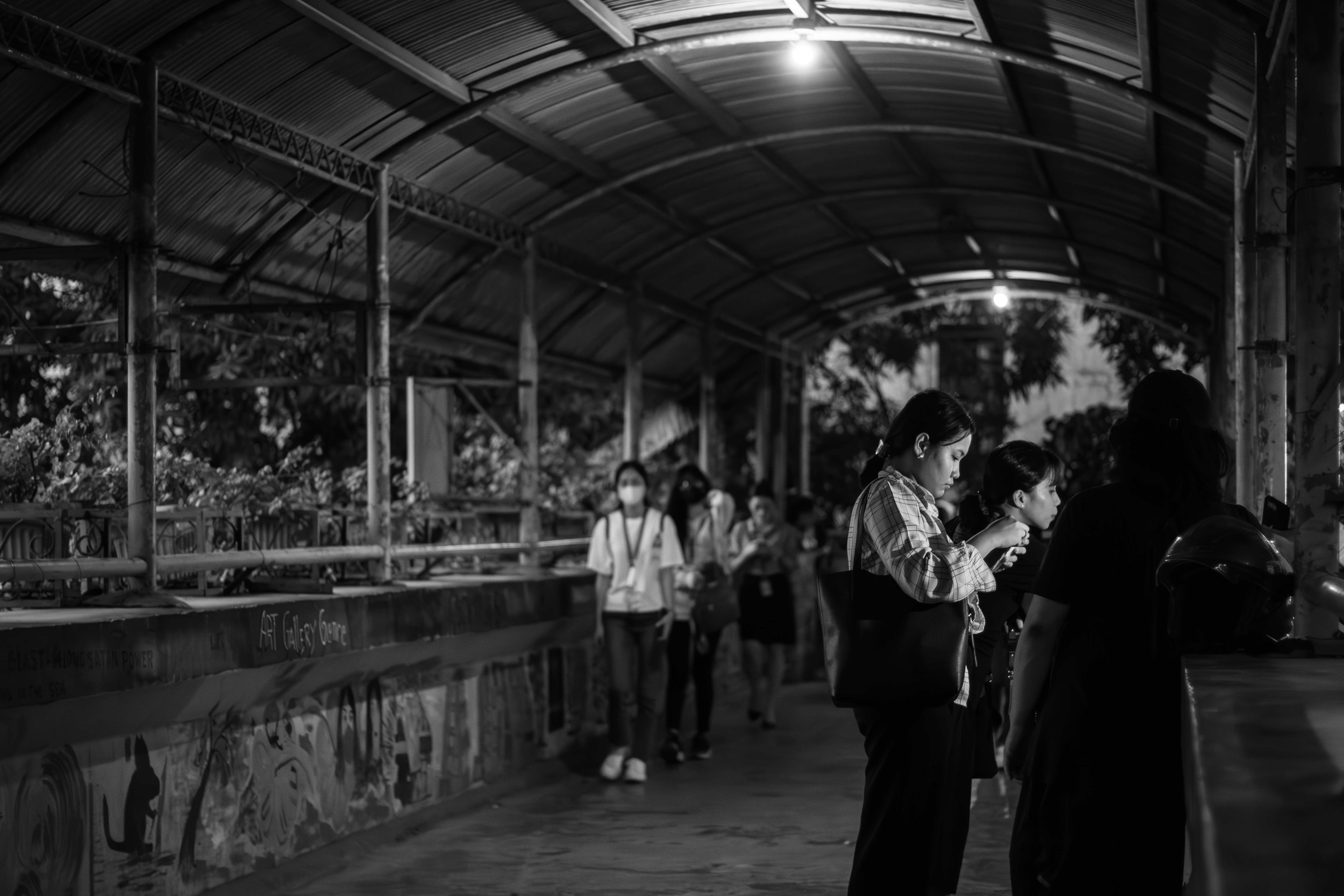 A monochrome scene capturing individuals engaged in their own worlds while navigating a bustling walkway. The blend of figures creates a dynamic urban atmosphere.