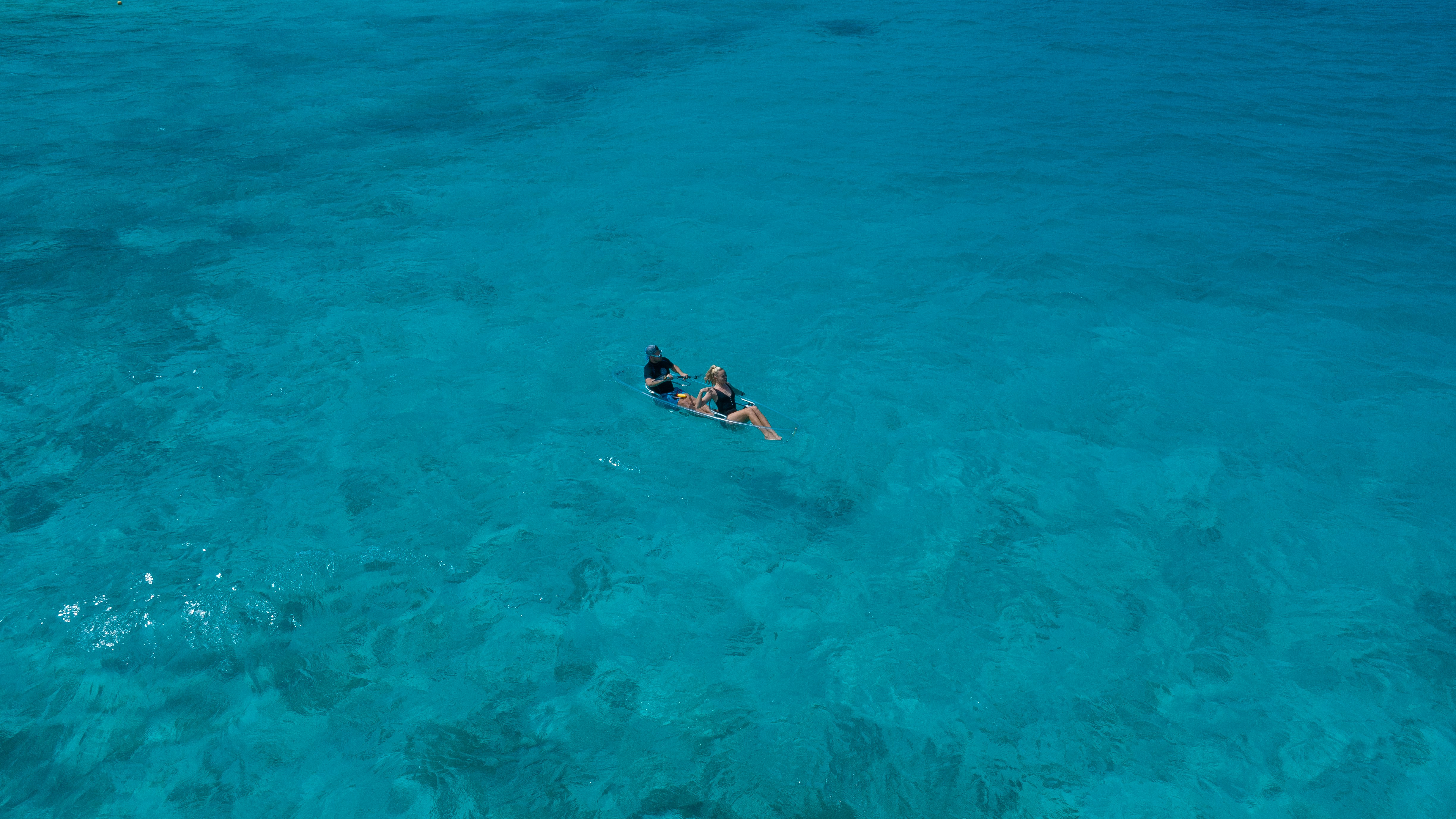 A couple kayaking in a transparent boat above crystal-clear turquoise waters of the Maldives. A peaceful and romantic tropical escape. | A kayaker is floating on the turquoise ocean.