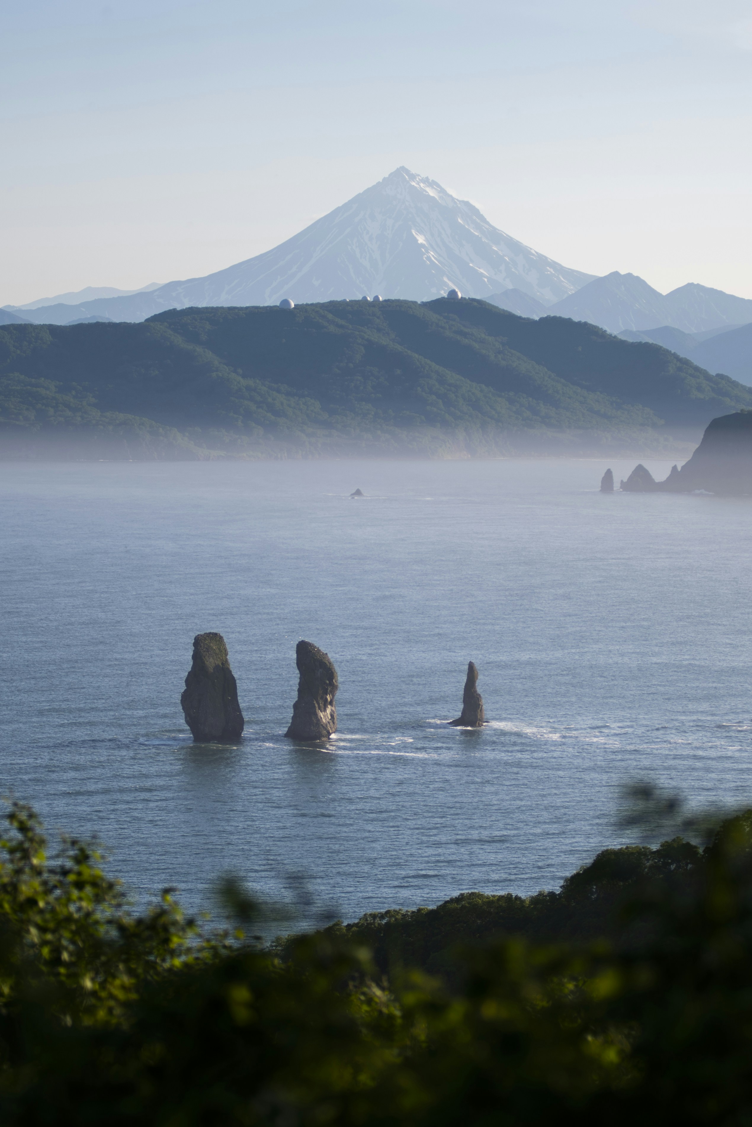 Volcano towers over sea stacks in a misty landscape. photo – Free Blue ...