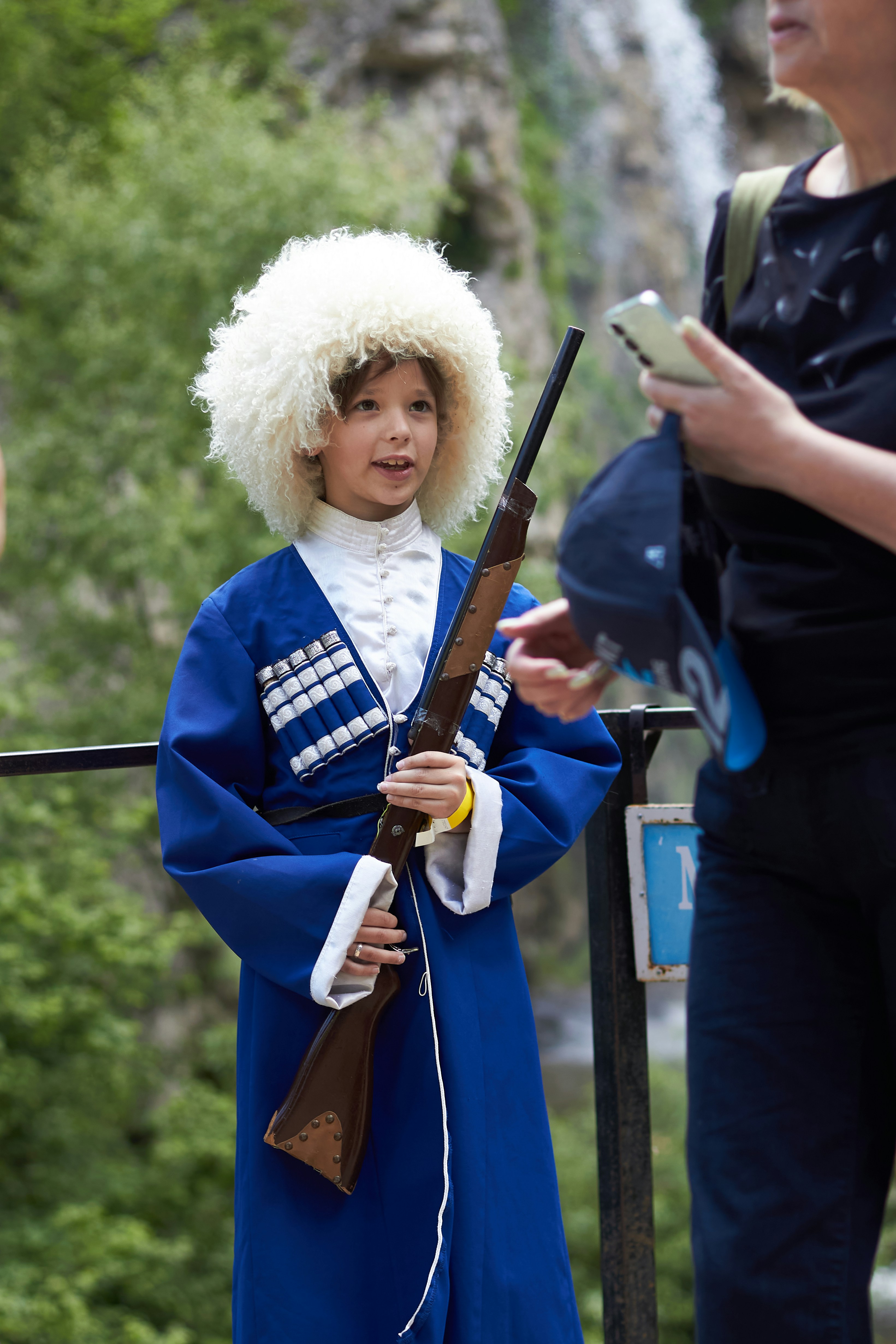 A boy in traditional attire holds a rifle.