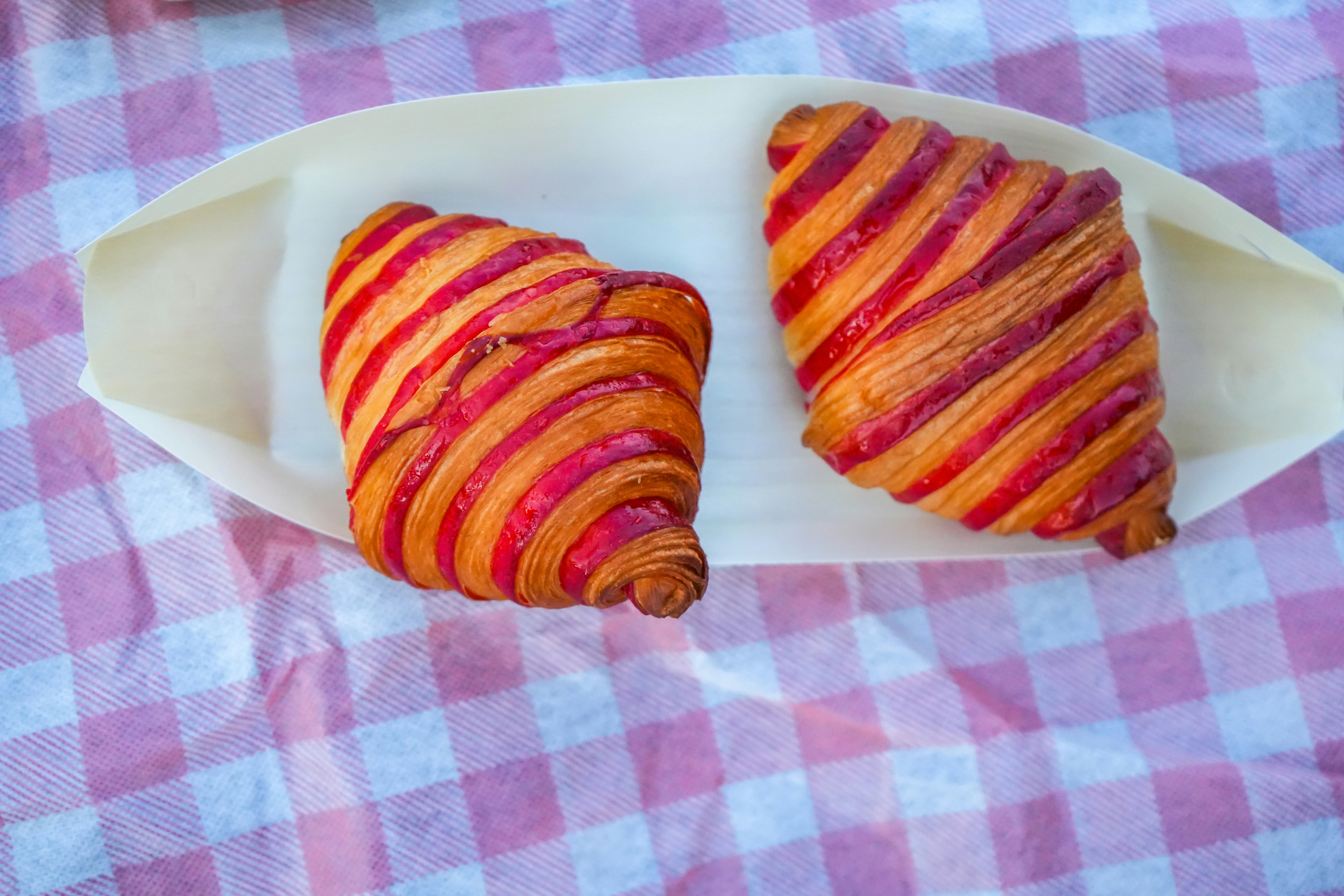 Cozy summer picnic on a checkered blanket with fresh fruits and buttery croissants, set in nature. A perfect mix of rustic charm and outdoor relaxation. | Two colorful croissants are placed on a plaid cloth.