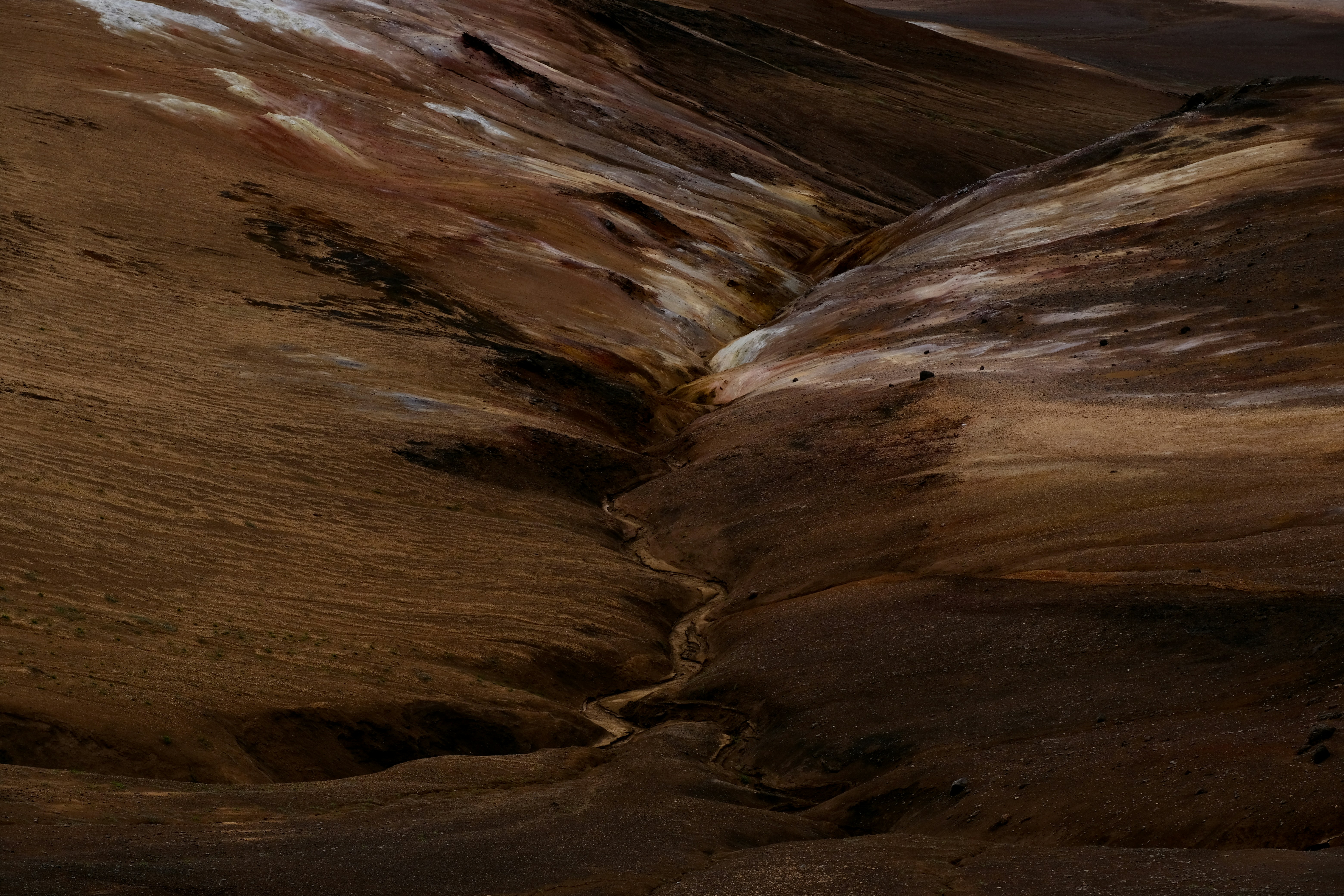 Abstract landscape featuring rich, earthy tones and intricate patterns formed by geological processes. The image highlights the natural beauty of the terrain.