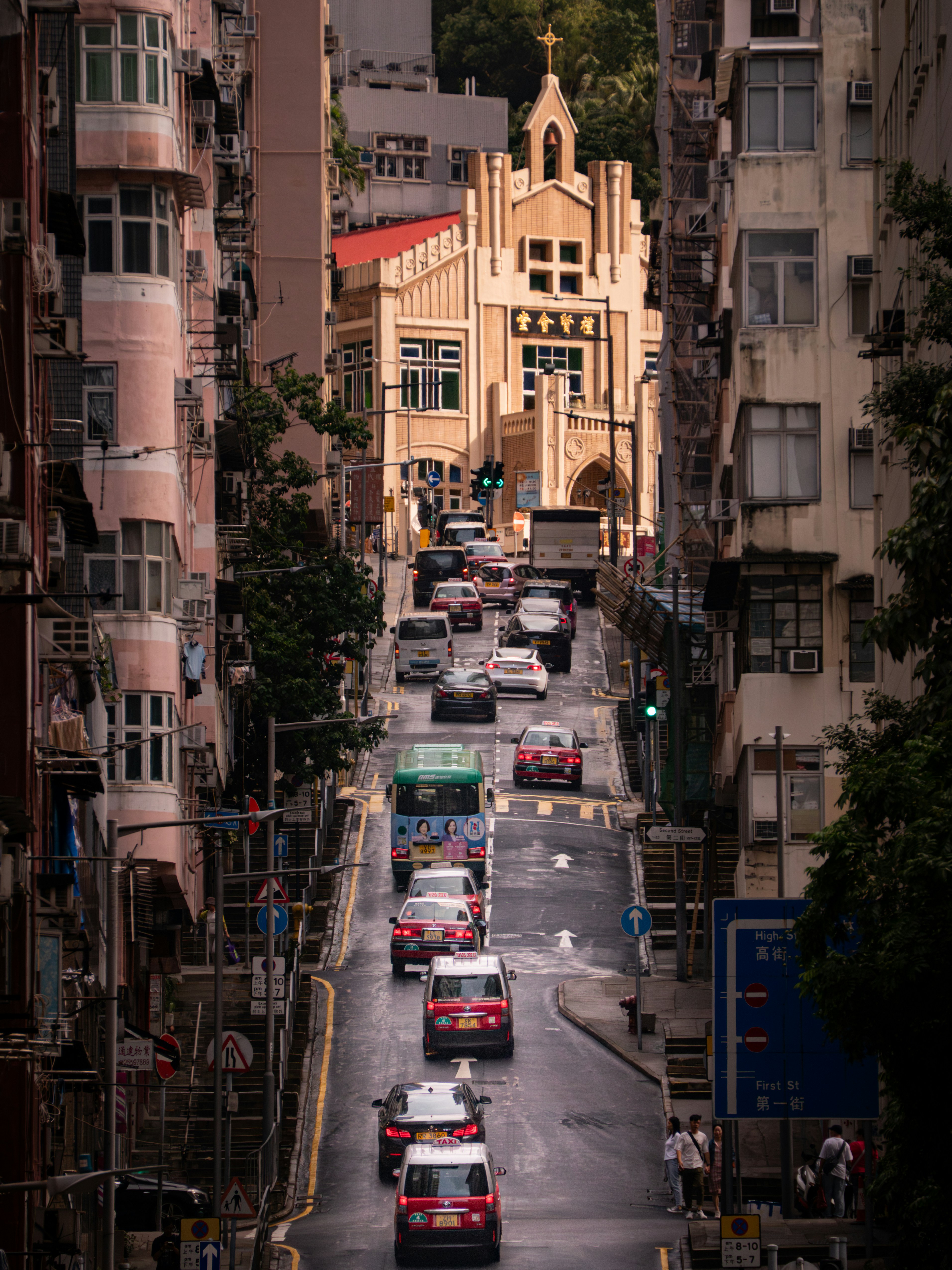 Busy street scene in an urban area, featuring a church at the end of the road surrounded by vehicles and buildings. Traffic lights and signs add to the bustling atmosphere.