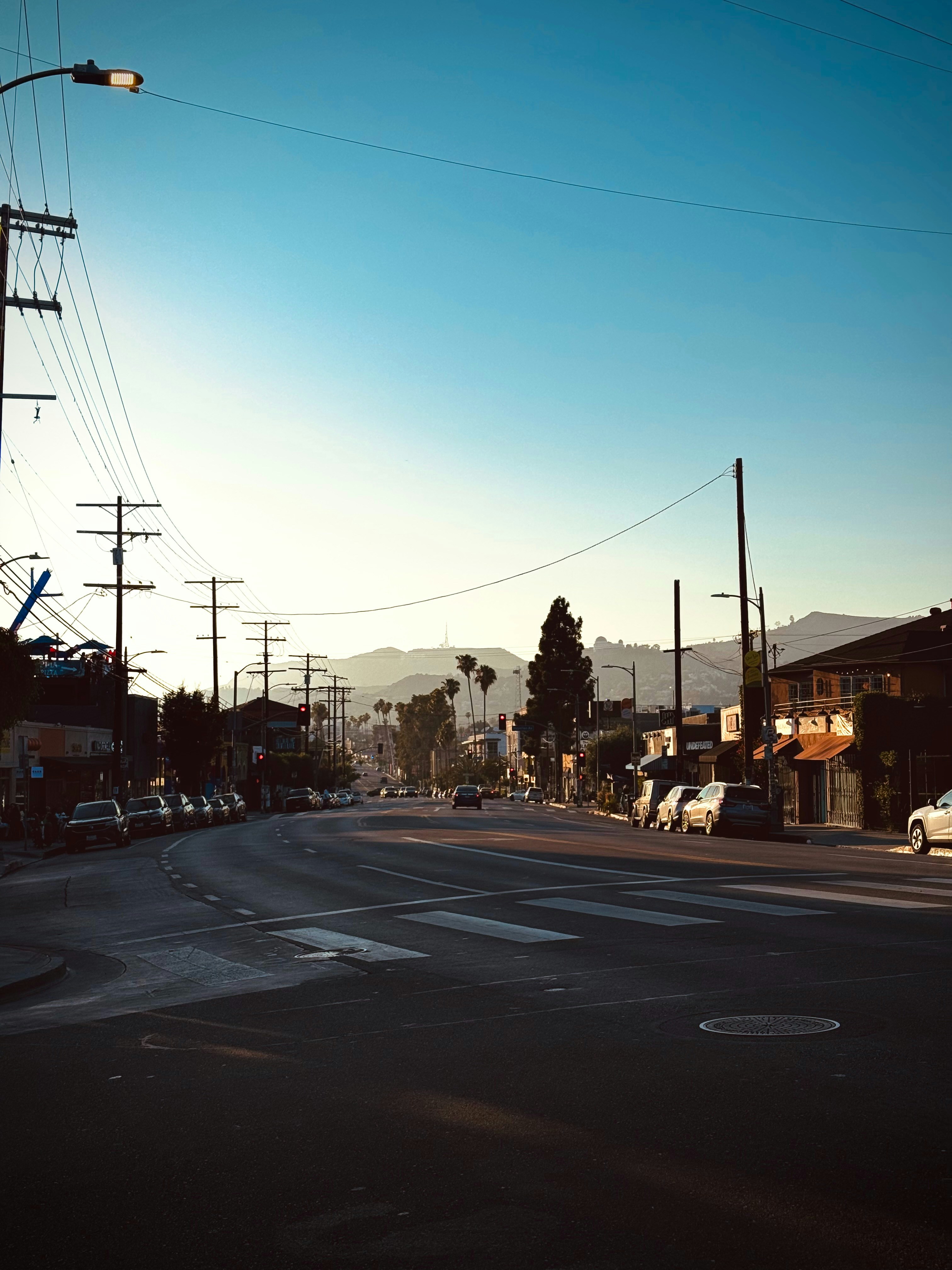 A quiet city street bathed in the warm light of dusk, with silhouettes of palm trees and distant hills creating a tranquil urban landscape.