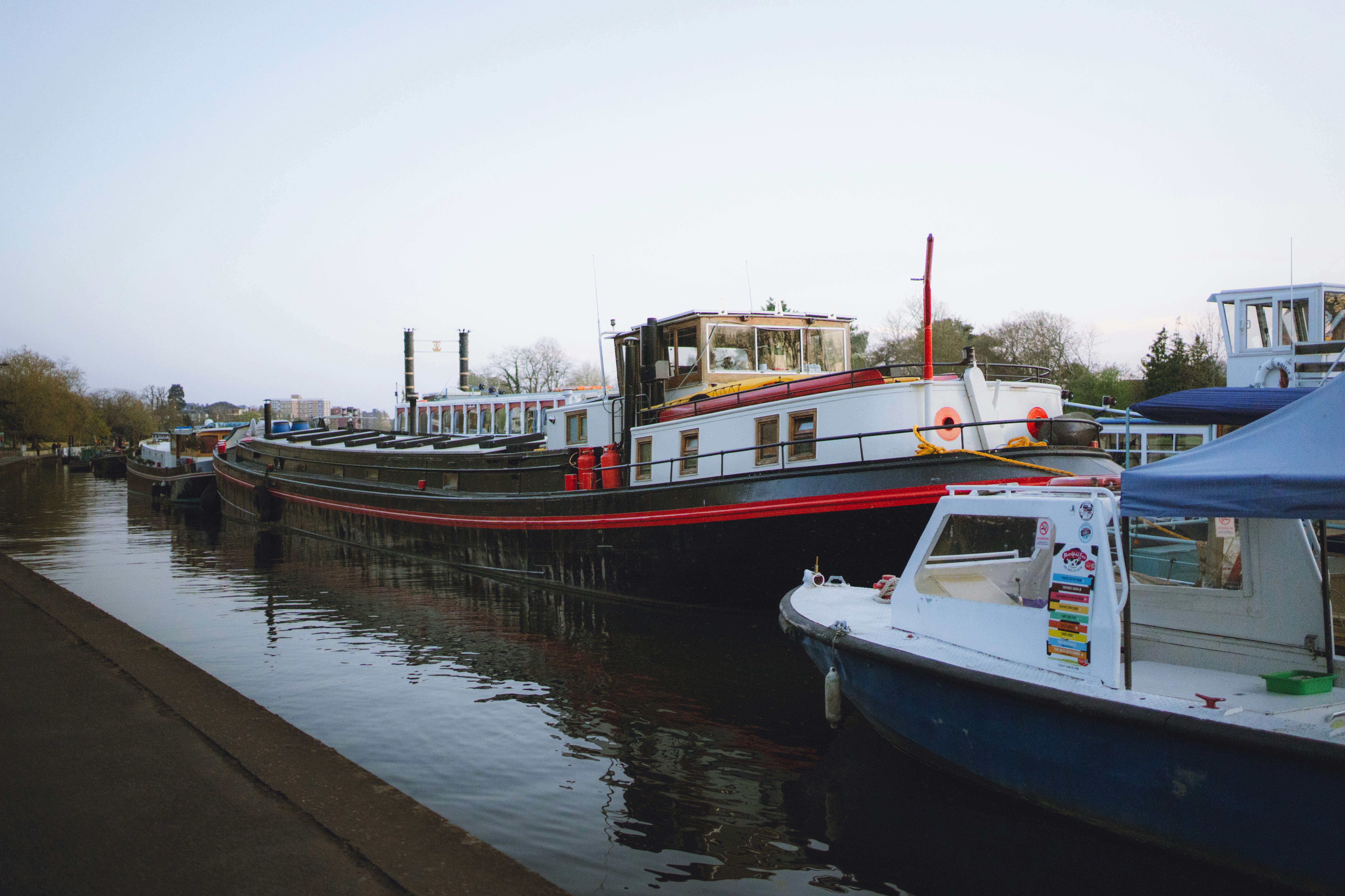 Two moored boats reflect on calm waters in a serene harbor setting during dusk.