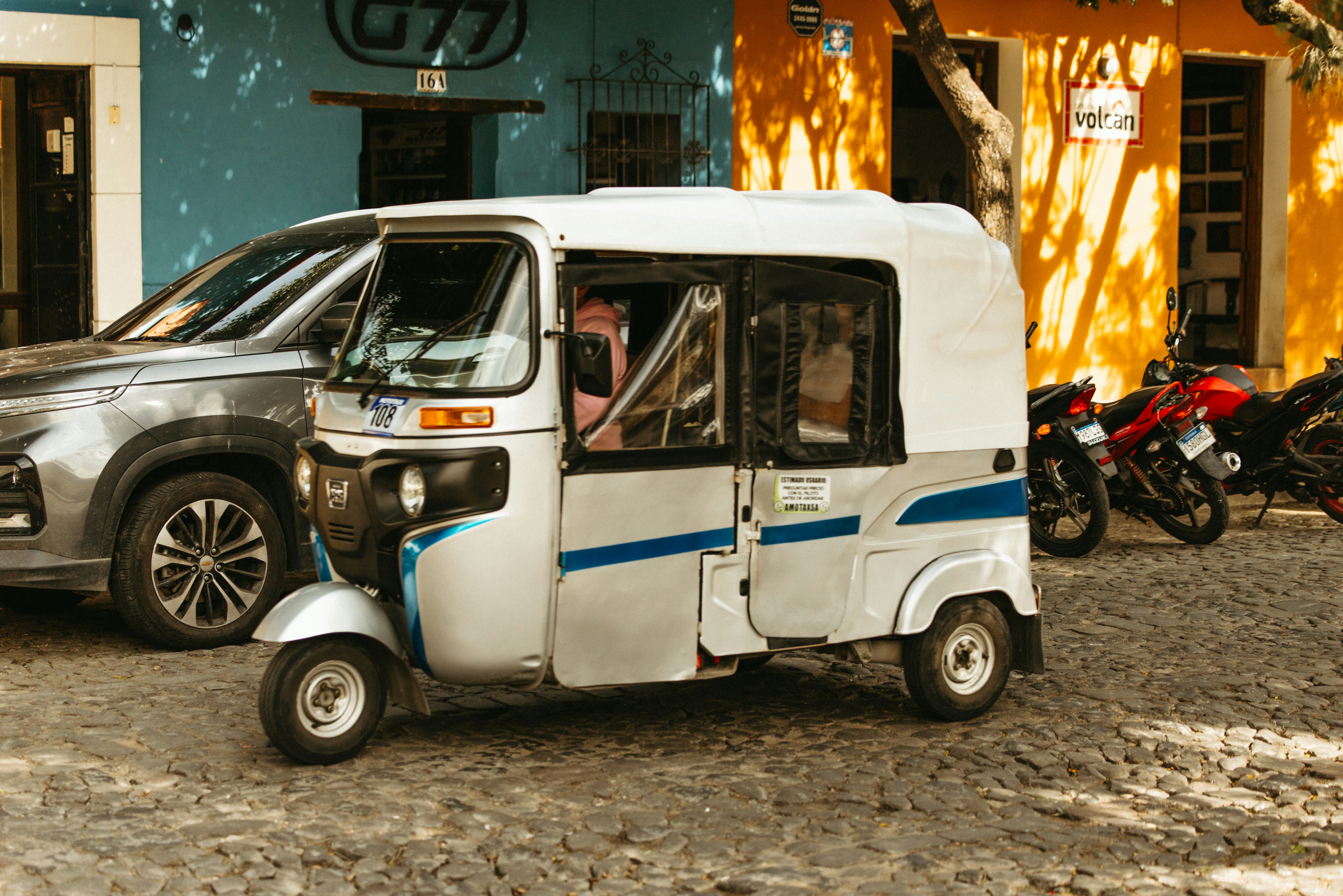 A white tuk-tuk is parked on the street.