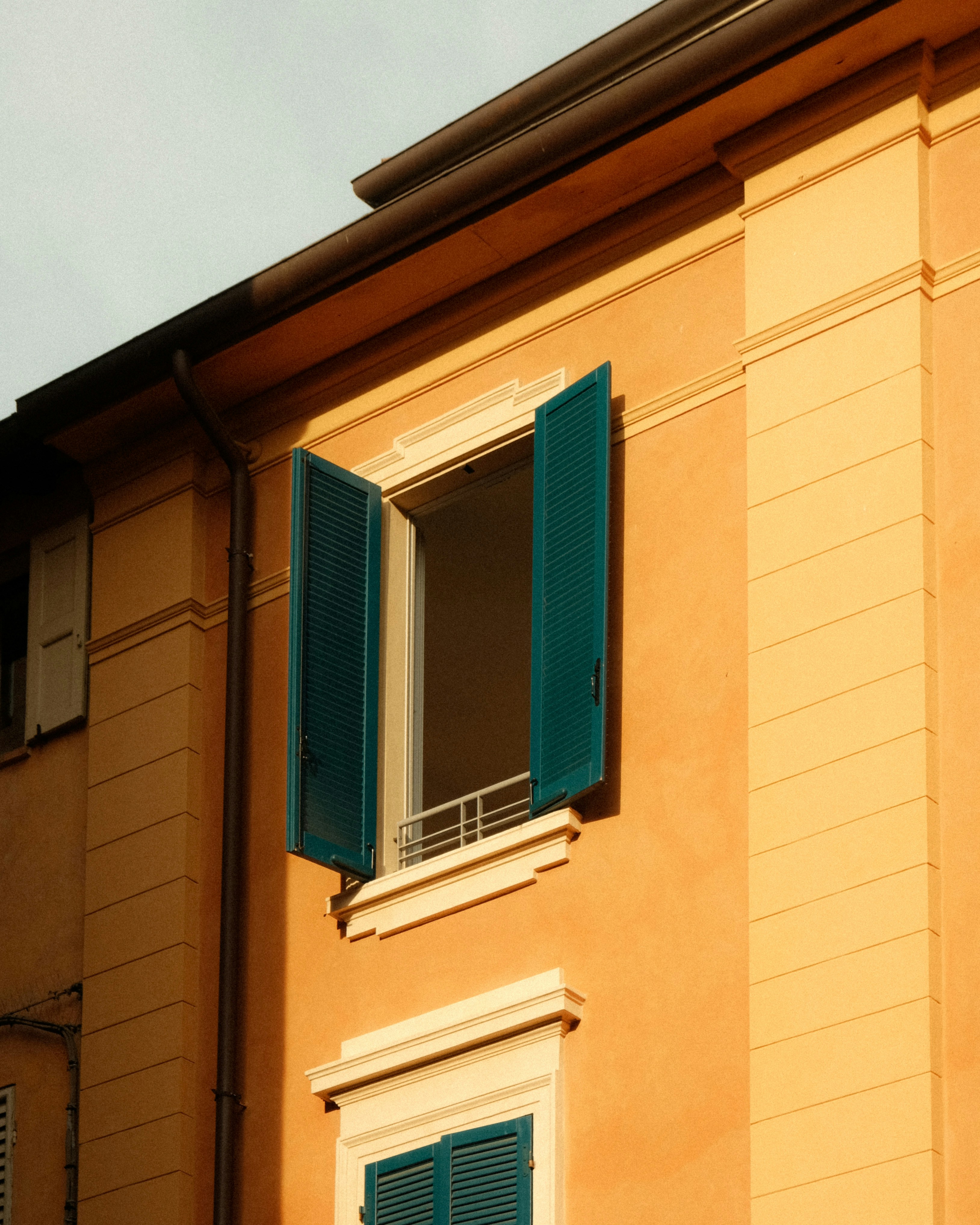 Open window with green shutters on an orange building.