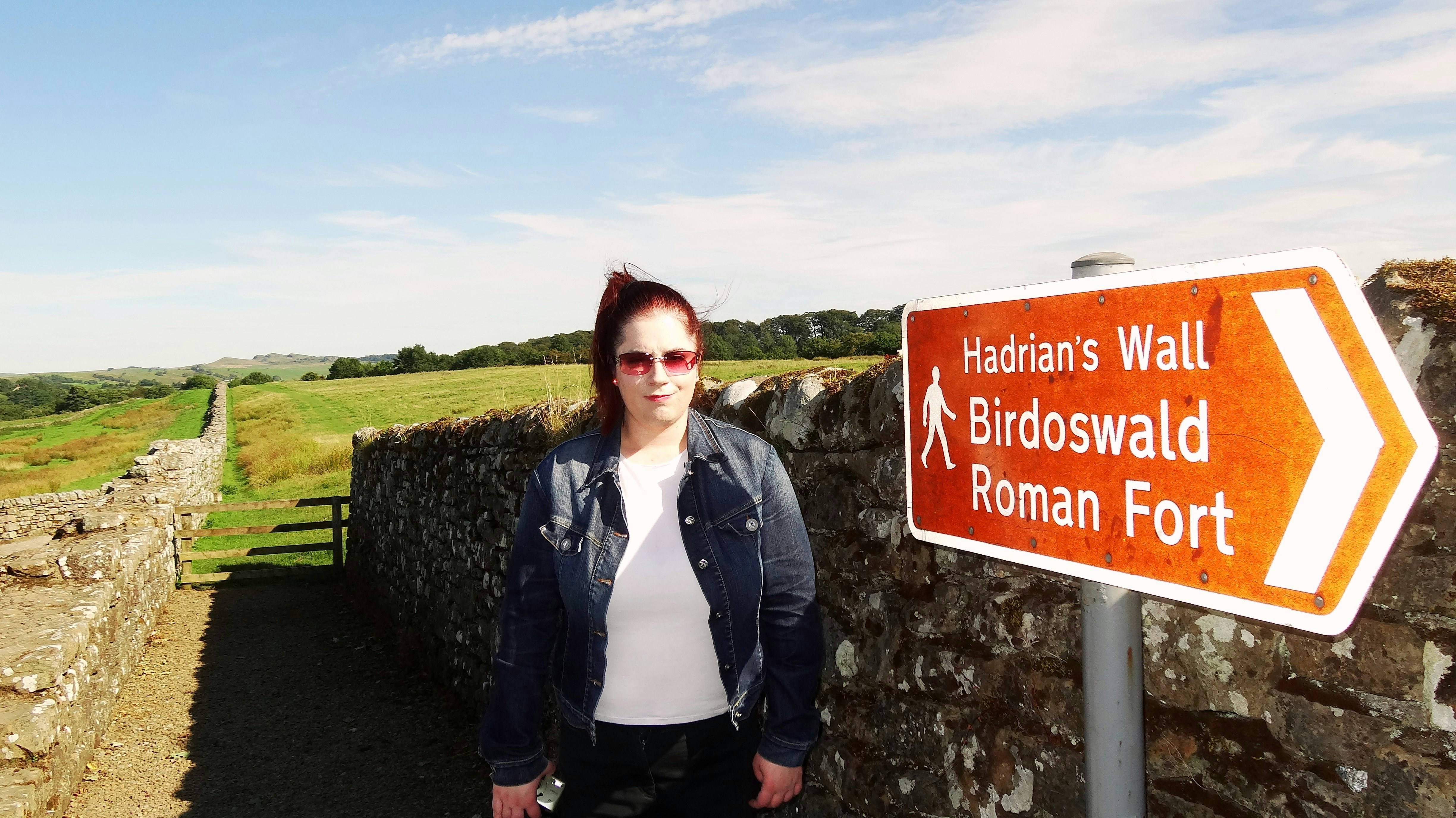 taken september 4th 2019 | A woman stands near a sign for hadrian's wall.