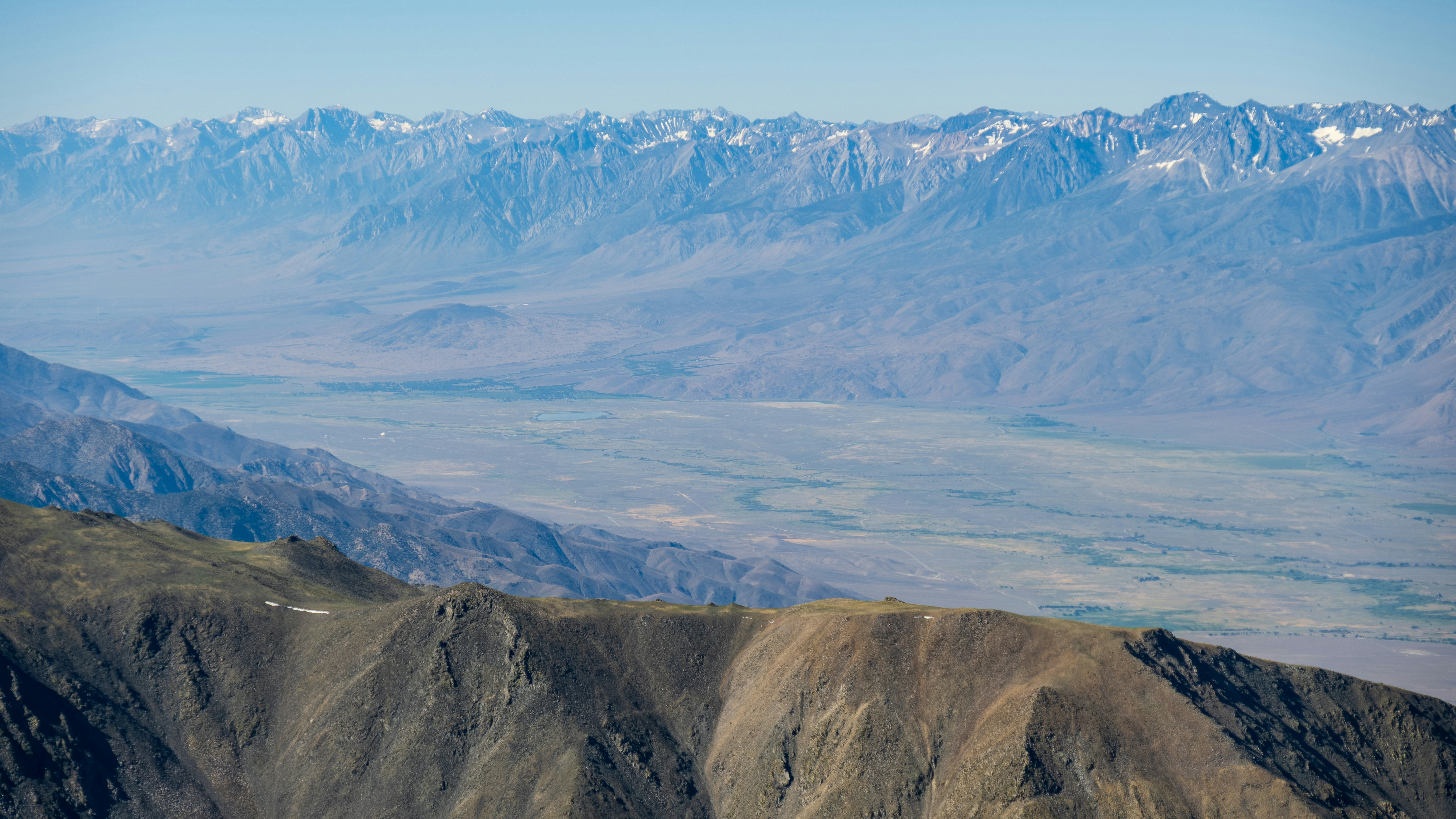 At the summit of White Mountain Peak looking South West toward the Palisades | Mountain peaks tower over a hazy valley.