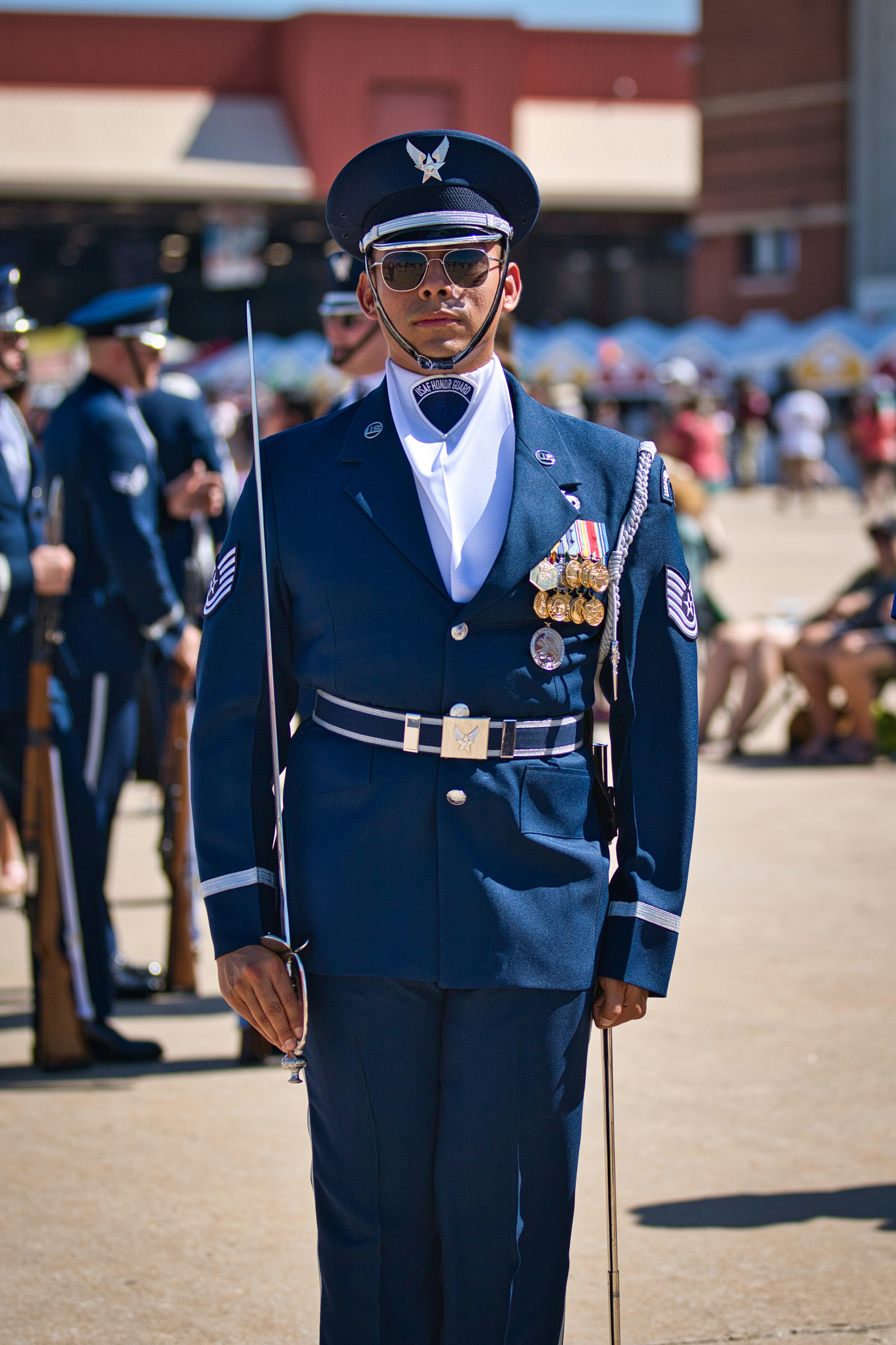 Air Force service member in formal uniform stands proudly during a ceremonial event, adorned with medals and holding a ceremonial sword.