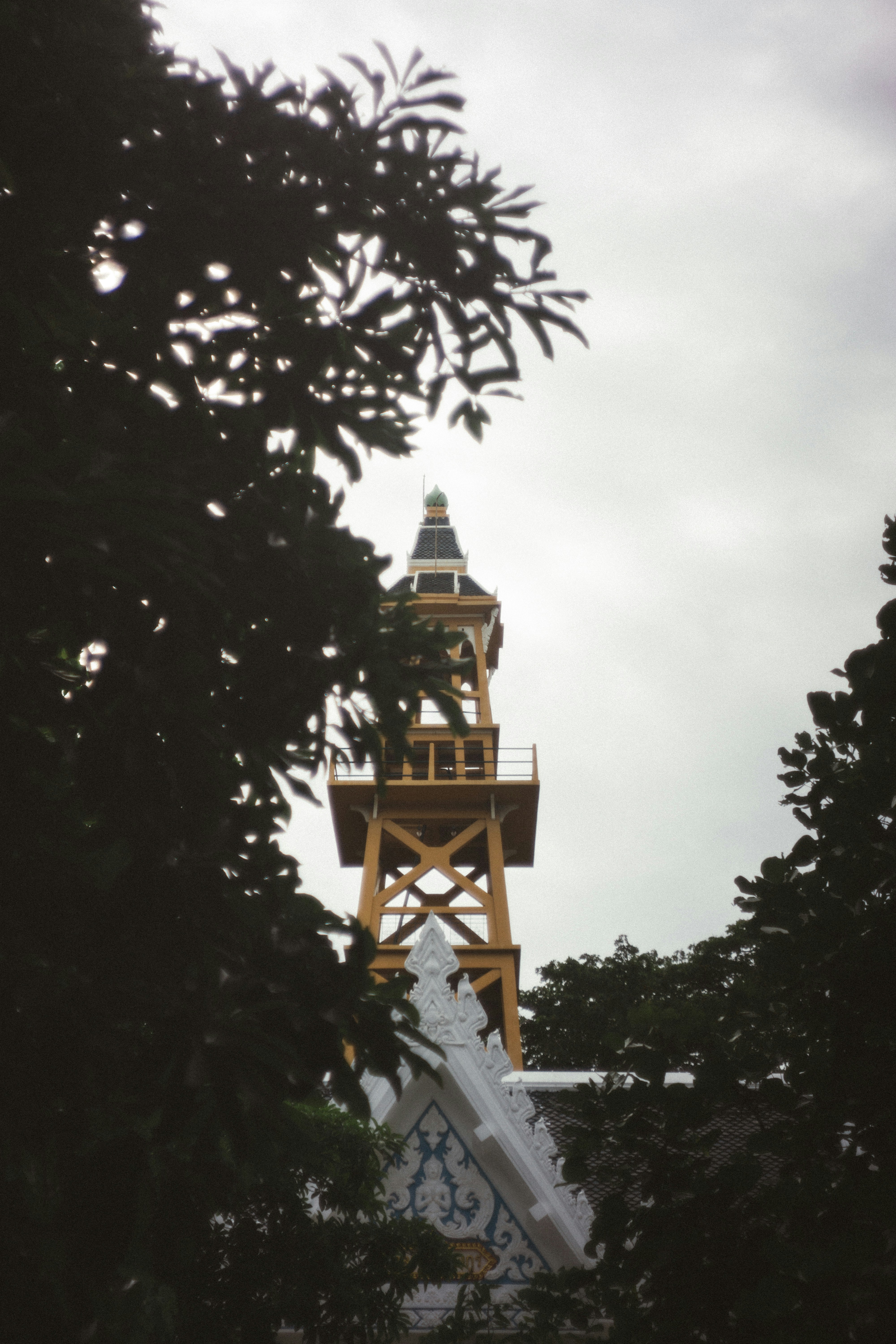 A tall structure framed by trees against a cloudy sky.