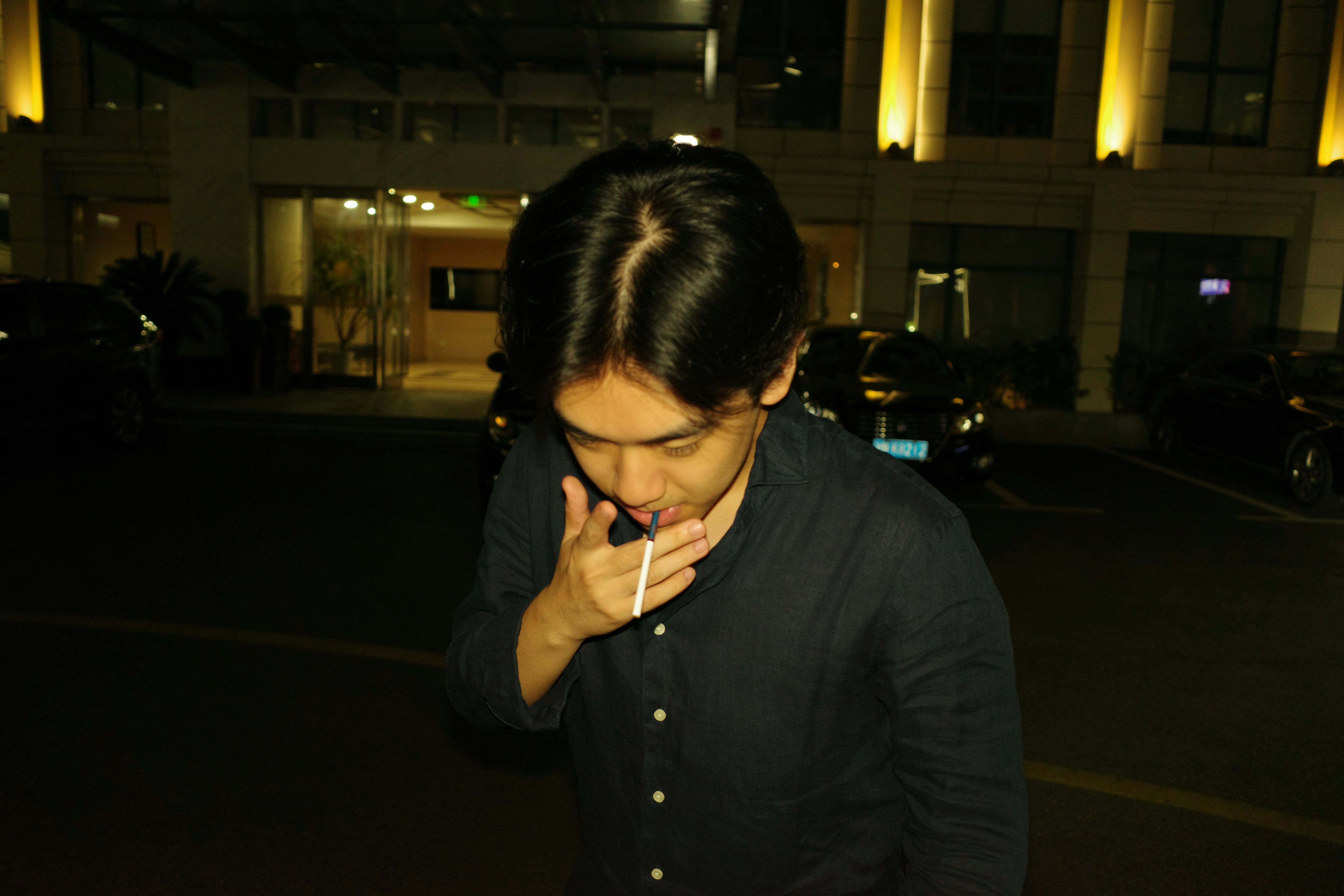 Individual thoughtfully engaging in a moment of reflection outside a modern building at night.