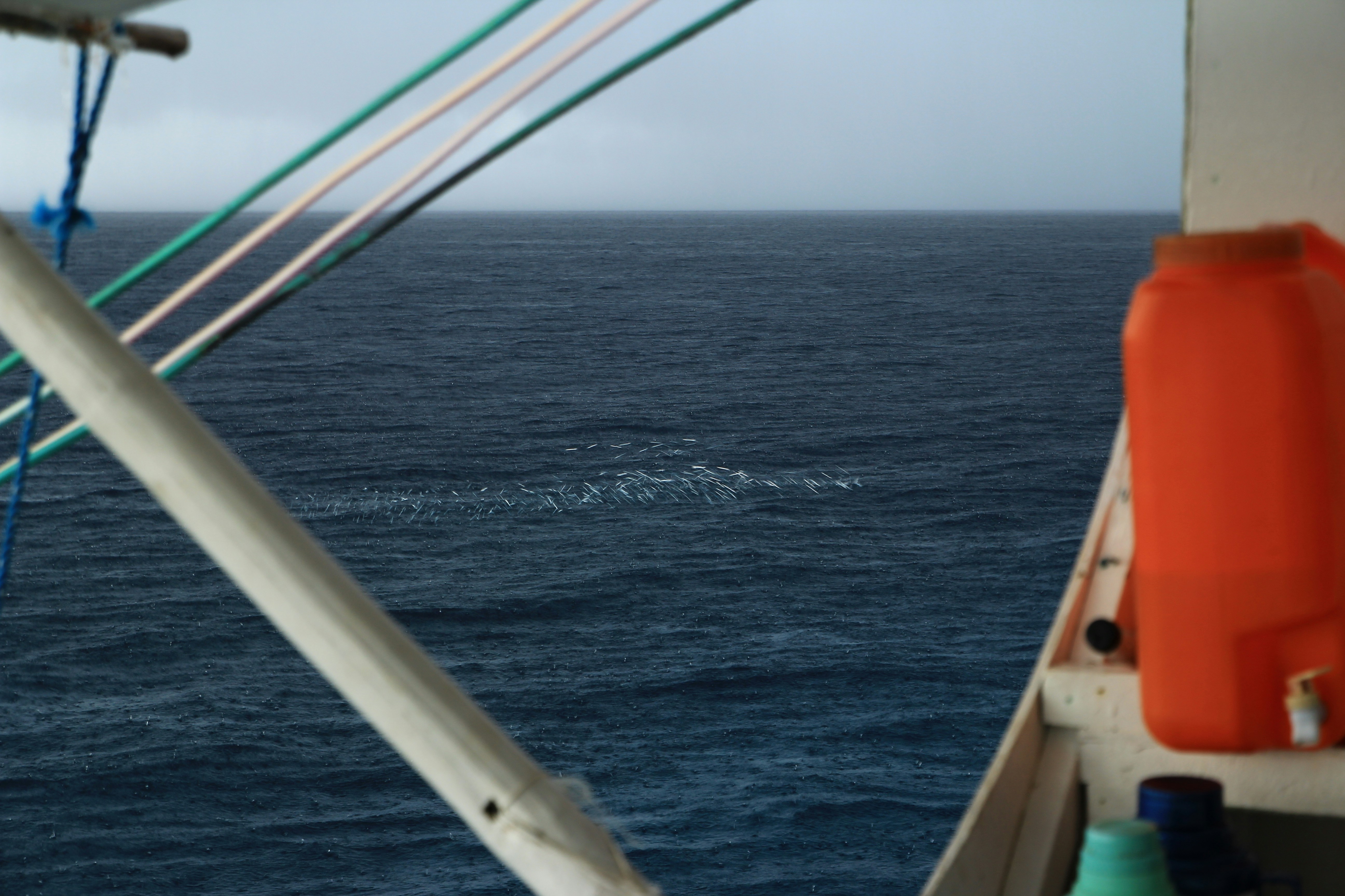 A view from a vessel showcasing the undulating waves of the ocean, with a vibrant orange container in the foreground. The scene captures the essence of maritime exploration.