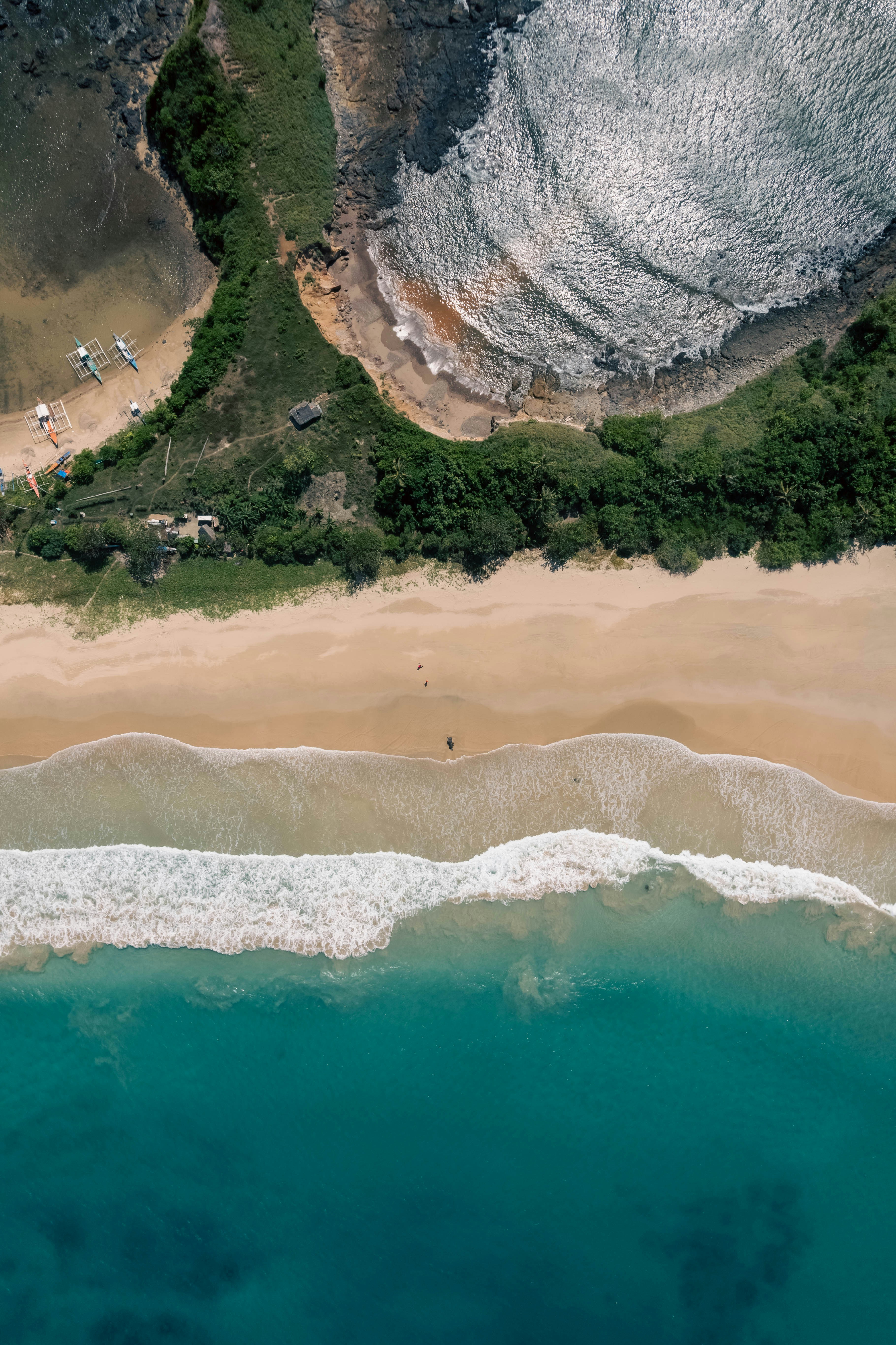 Aerial view of a tranquil beach scene, showcasing golden sands meeting turquoise waters, with lush greenery and rocky cliffs in the background.